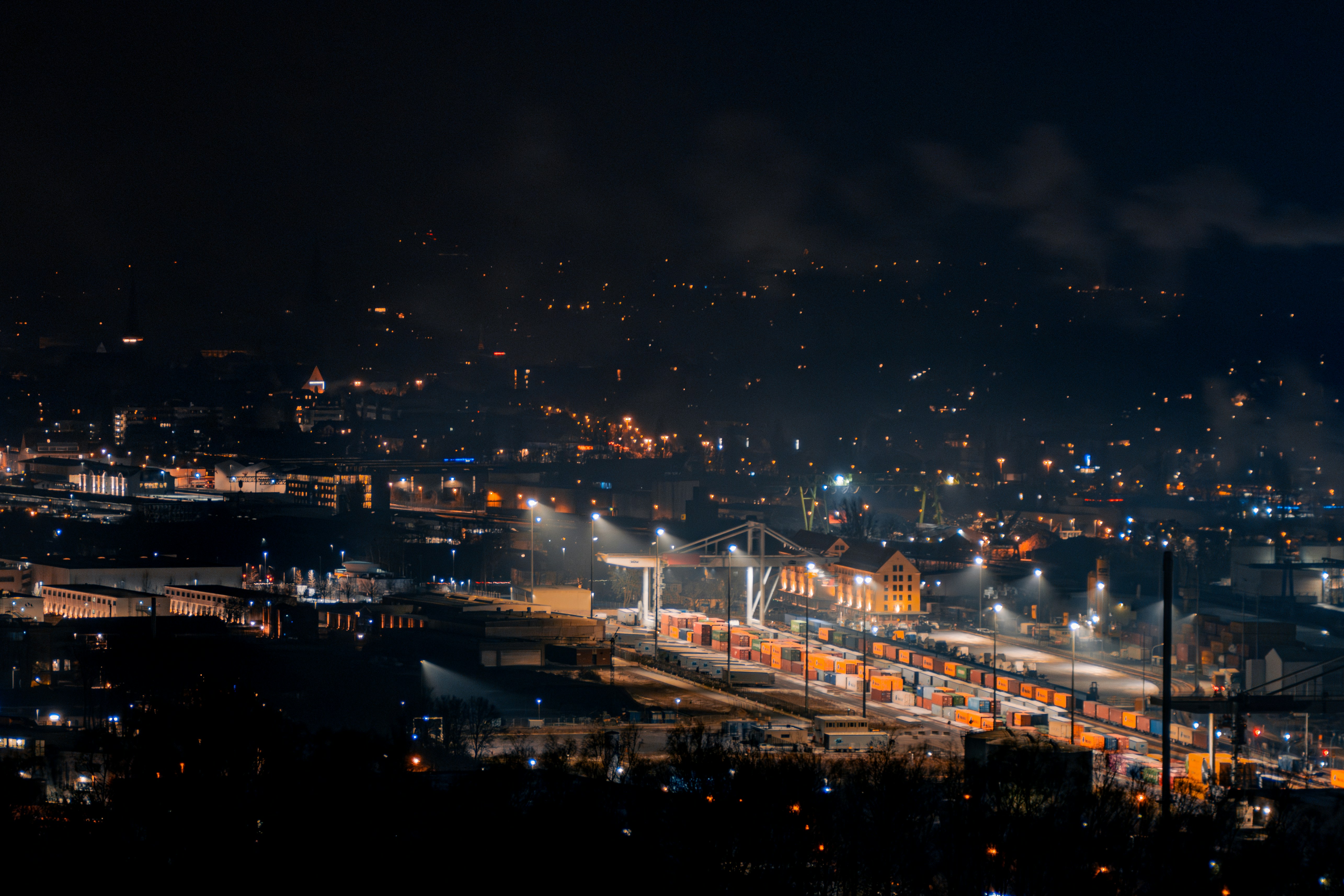 City skyline illuminated by industrial lights under a dark night sky.