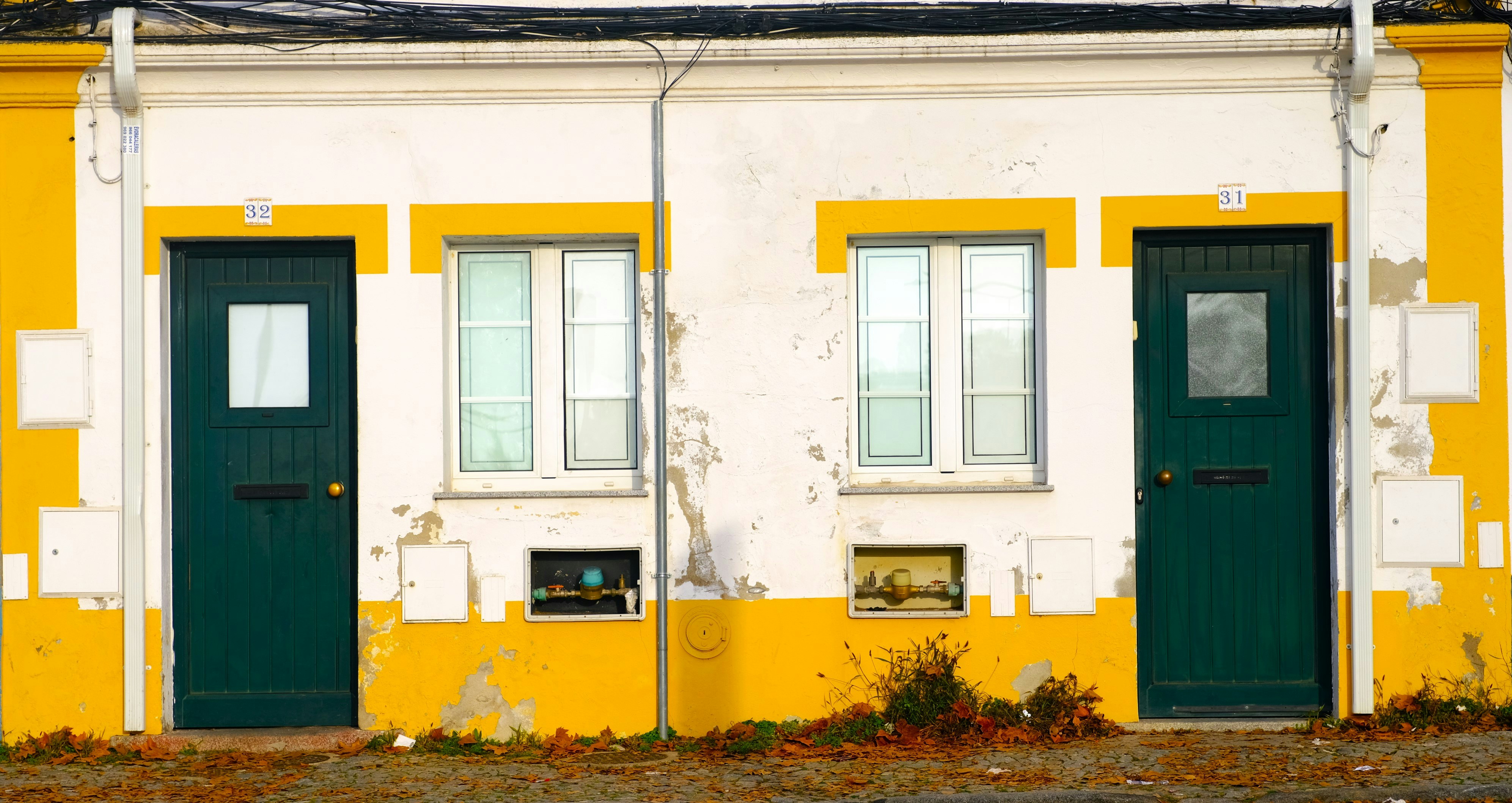 Two dark green doors and windows set against a weathered yellow and white facade.