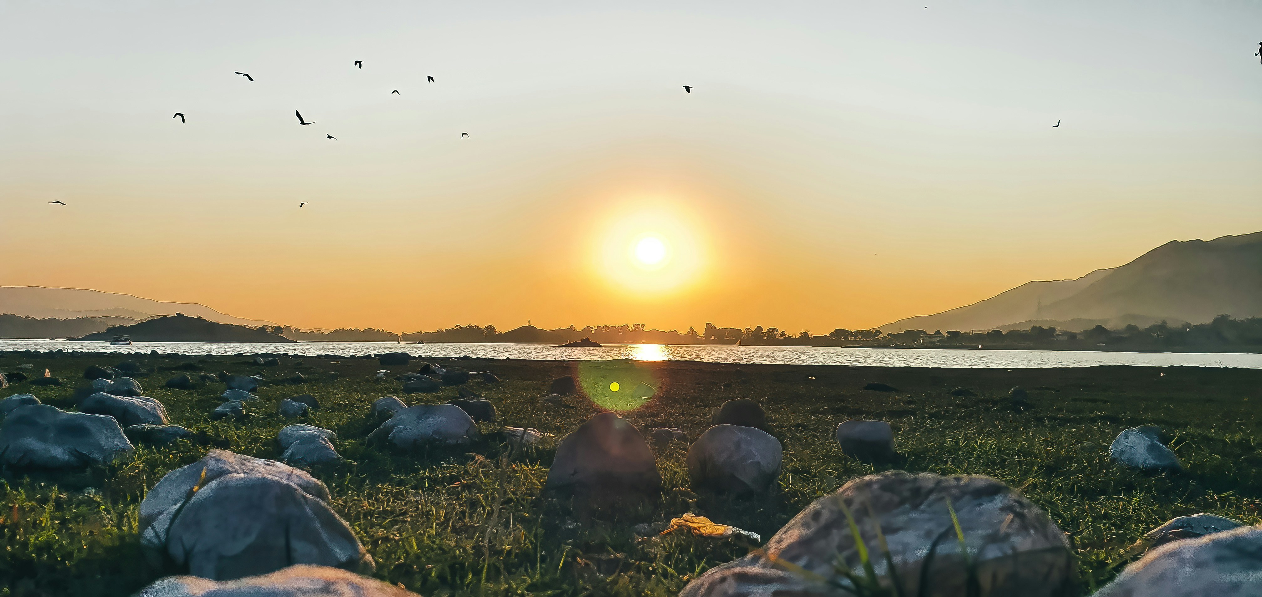 Dawn on the Pebble Shore: Sunlit Horizon over Quiet Mountains