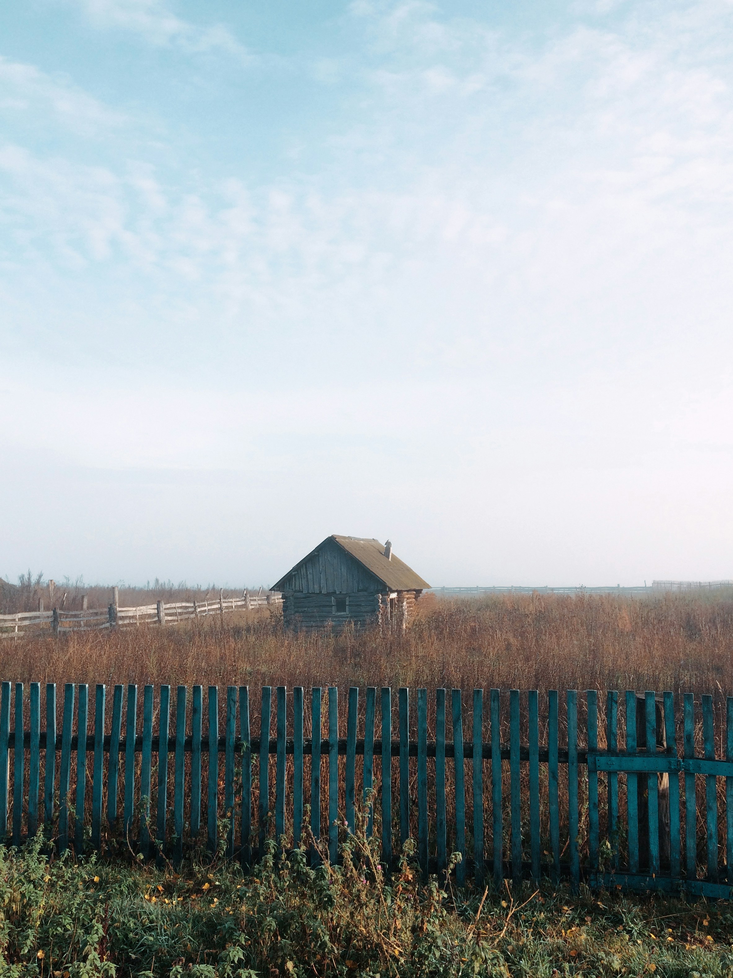 Horizon Cabin Behind a Weathered Fence in a Quiet Prairie