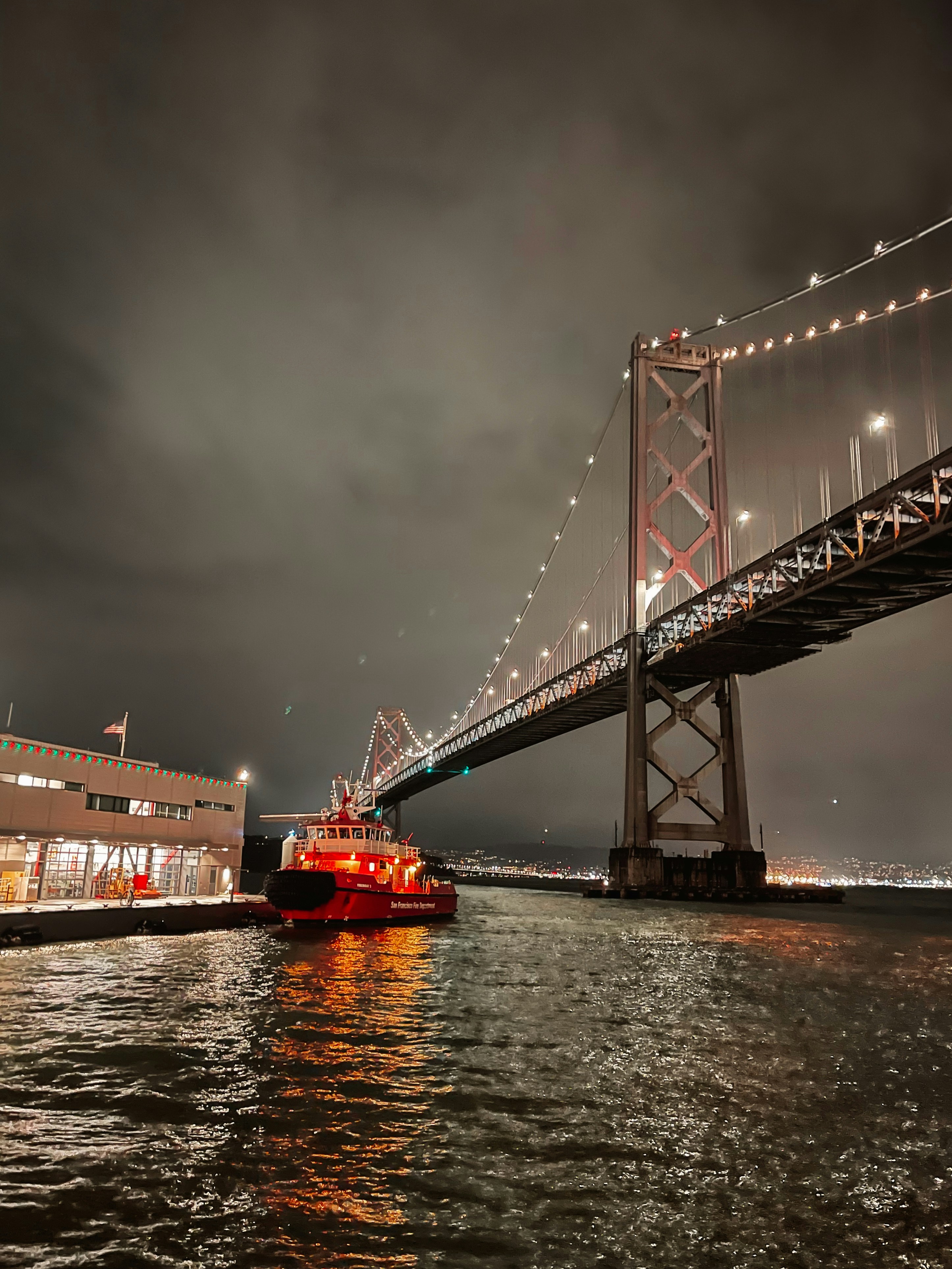 Red Tug Beneath a Lantern-Lit Suspension Bridge at Night