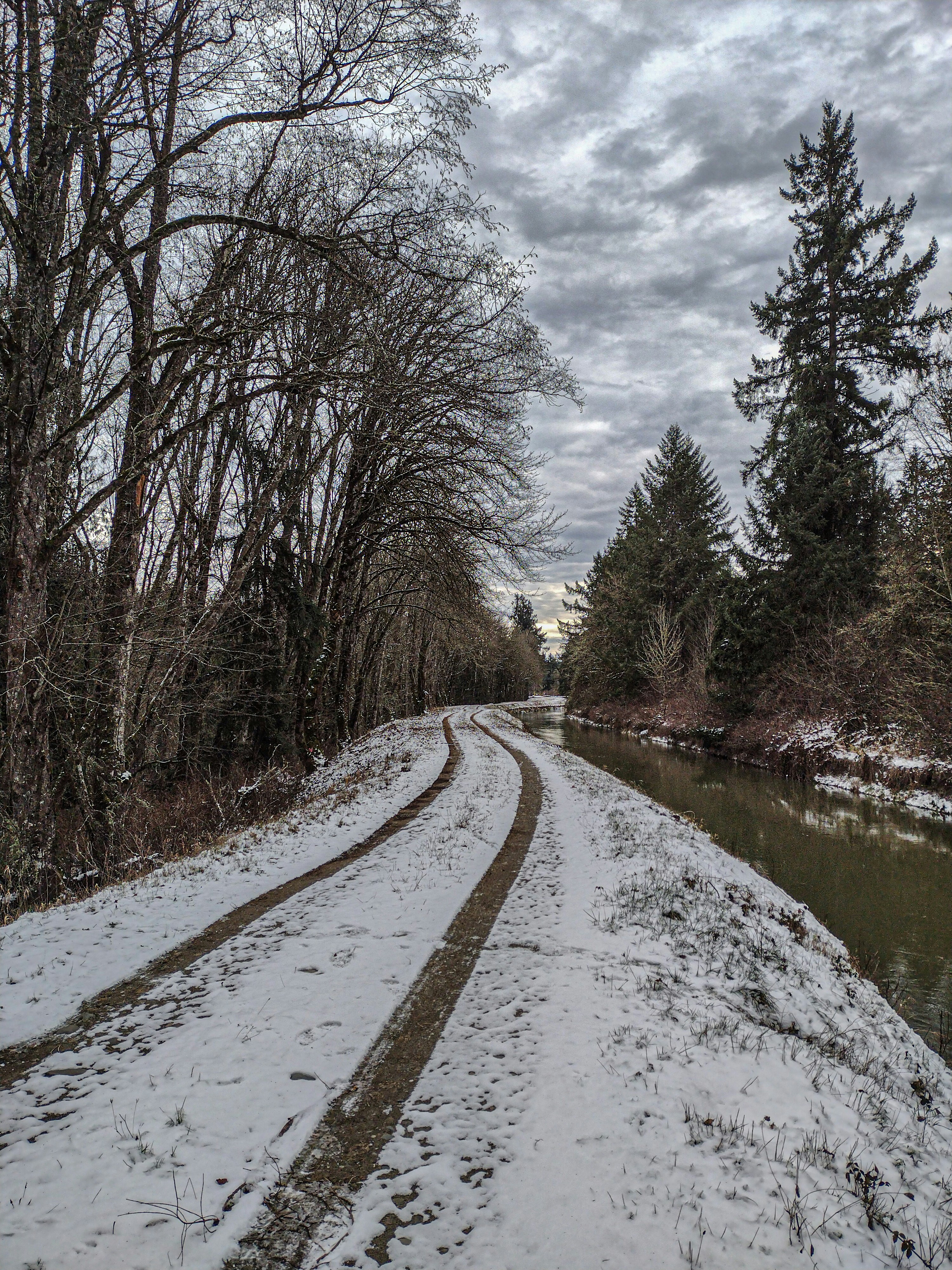 Snow-laced Path along a Riverbank under a Clouded Sky