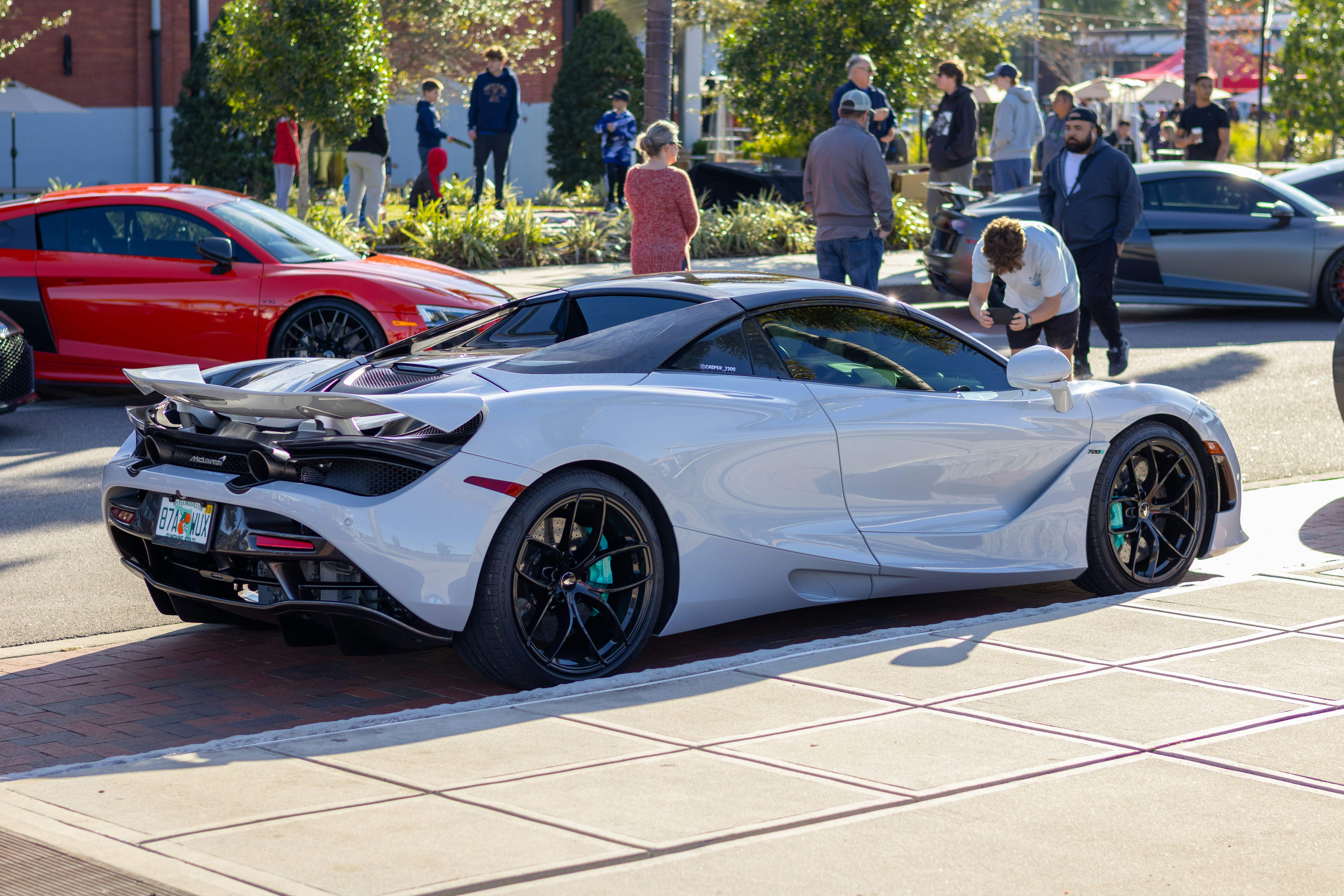 White hypercar on a sunny showroom plaza with onlookers