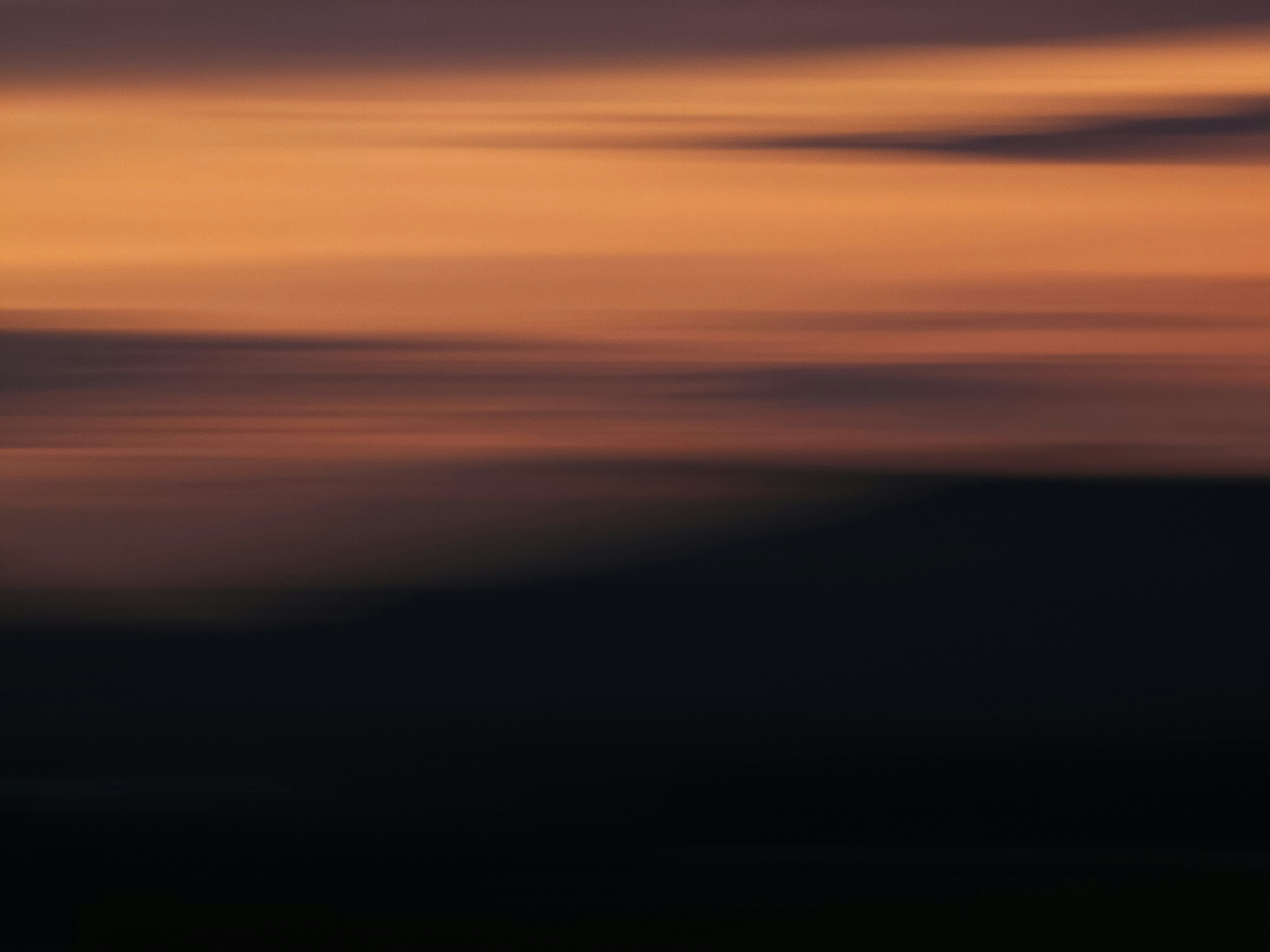 Motion-blurred desert landscape at sunset with a warm orange sky and dark dune silhouettes.