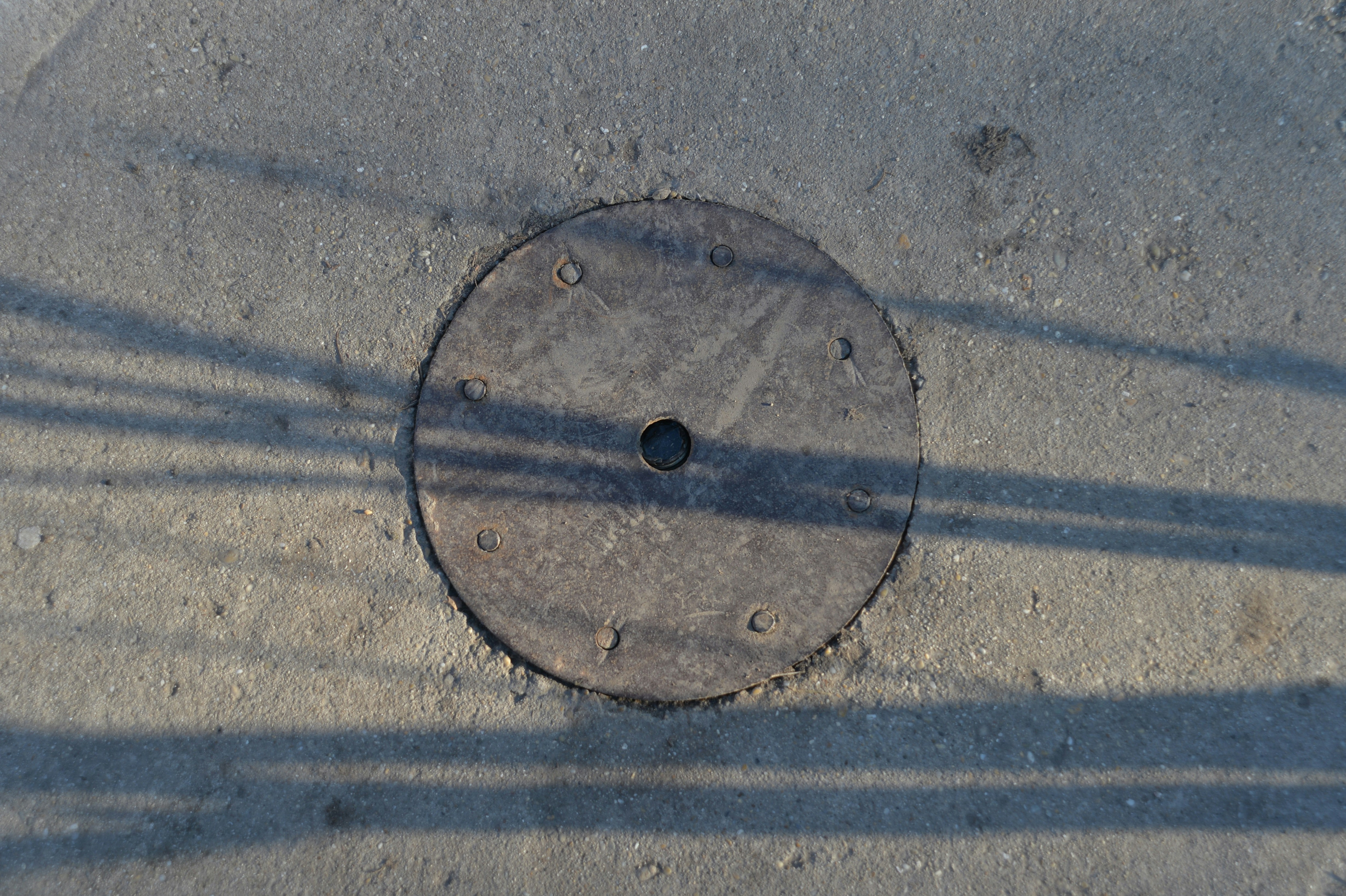 Center Circle in Concrete: Shadow Lines Crossing a Manhole Cover