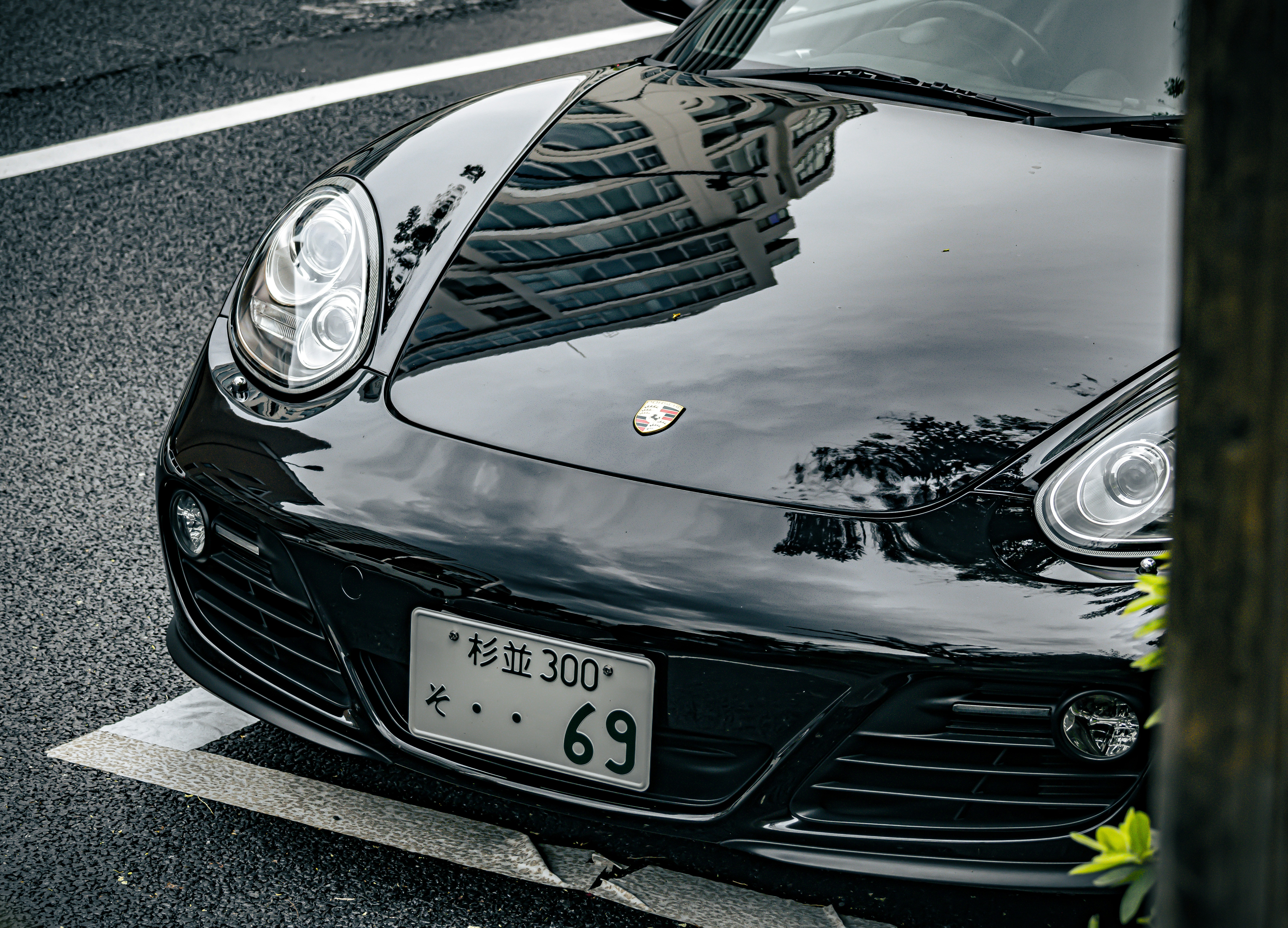 Close-up of a sleek black Porsche parked on a city street, reflecting nearby buildings and greenery.
