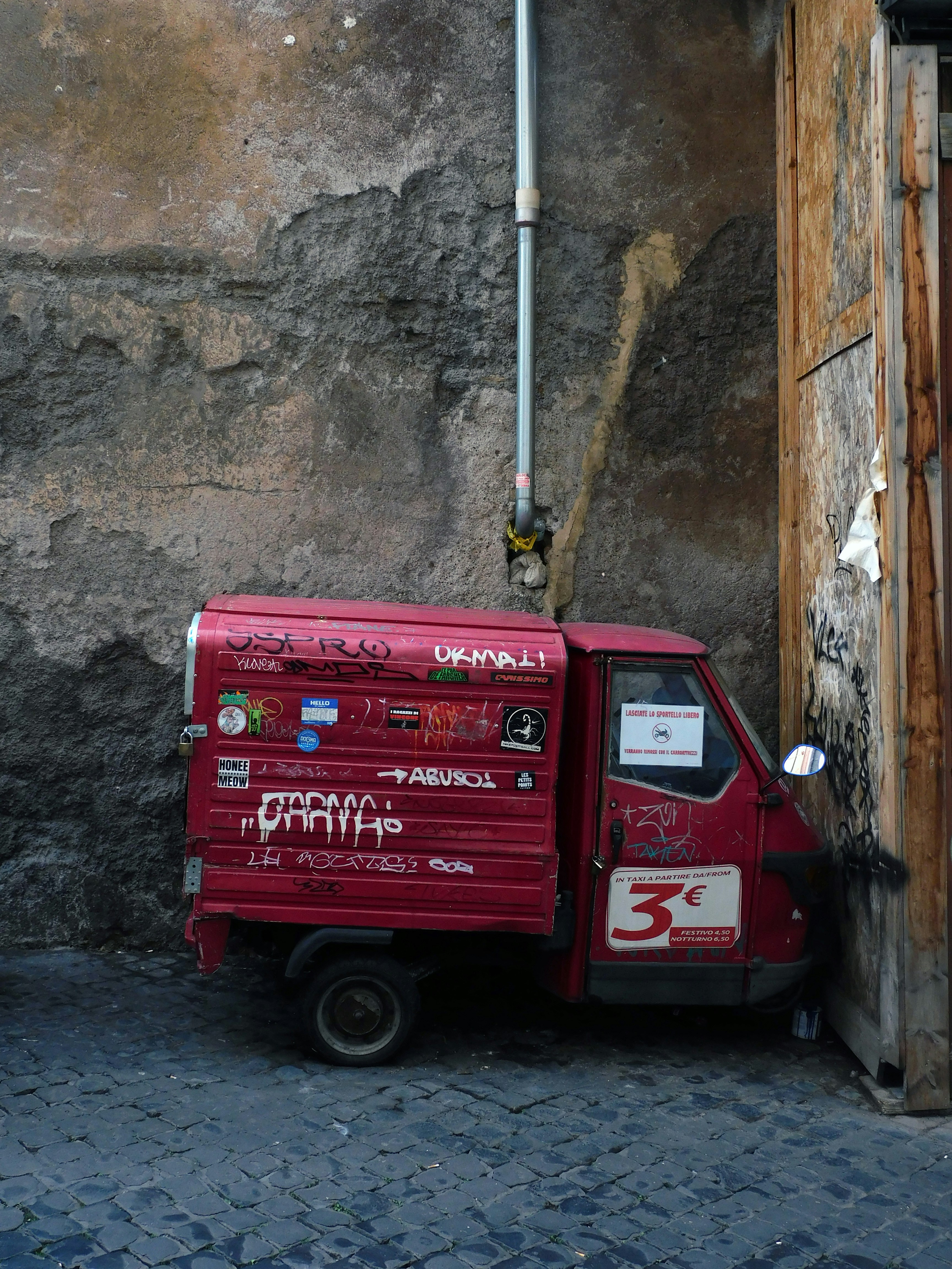 Crimson Courier: A Graffiti-Scarred Van Nestled Against a Timeworn Wall