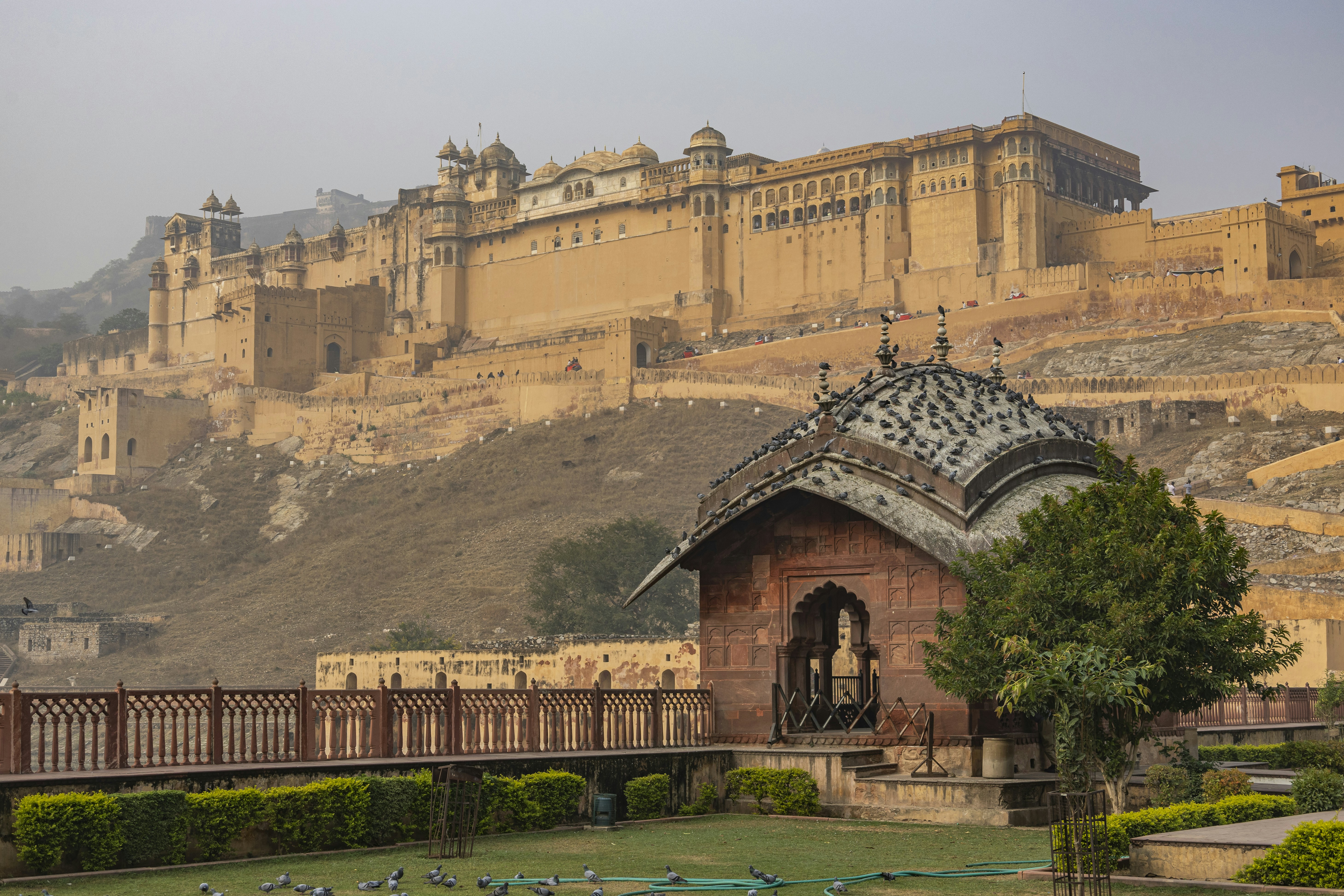 🏯Amber Fort towers above Ganpati Nagar in Jaipur, India, its sandstone façade glowing under the soft afternoon light. Set against distant hills and a sweeping lake, the fortress exudes regal strength and architectural elegance—an enduring symbol of Rajput legacy and craftsmanship.