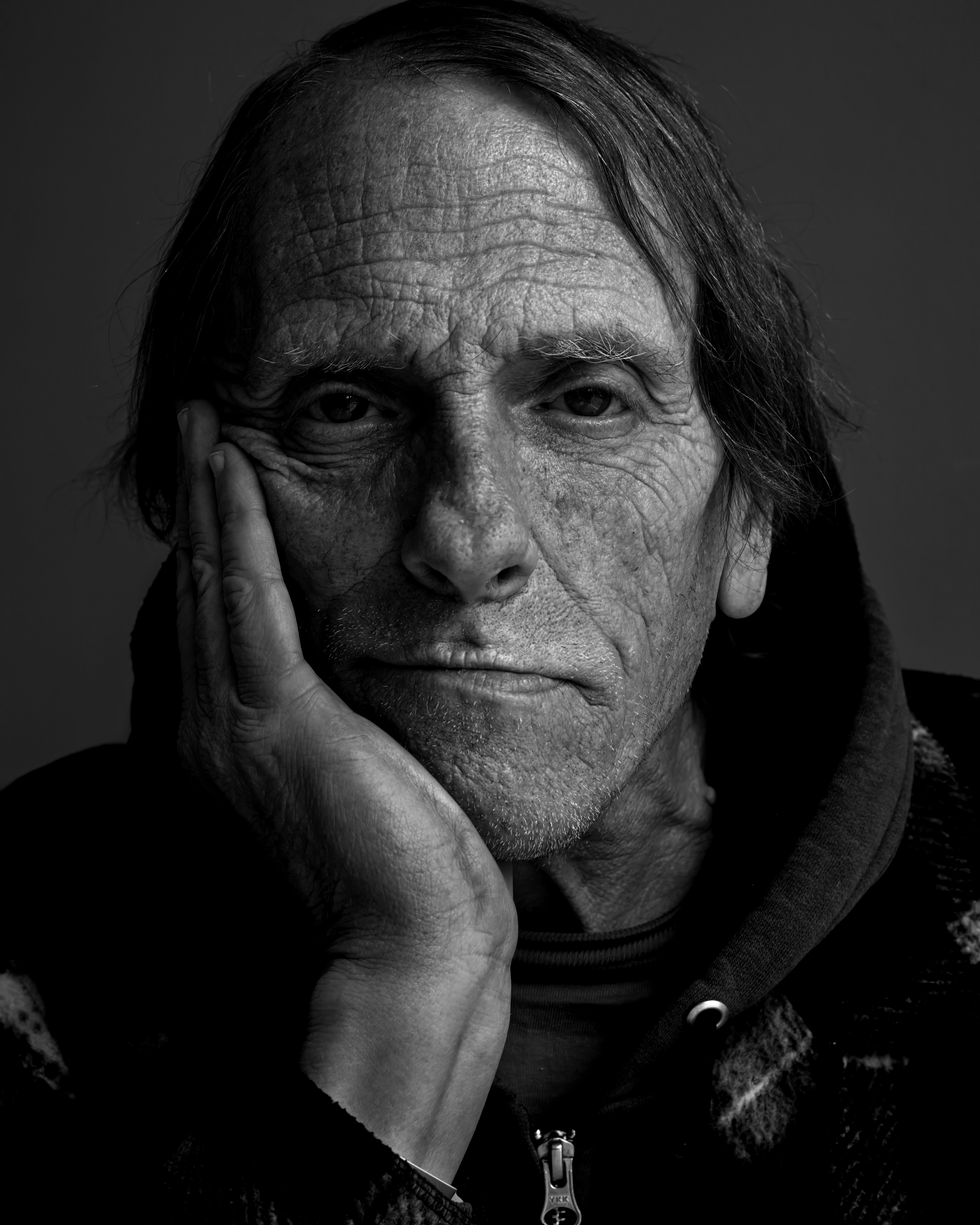 Worn wisdom in monochrome: a weathered gaze anchored by a quiet hand