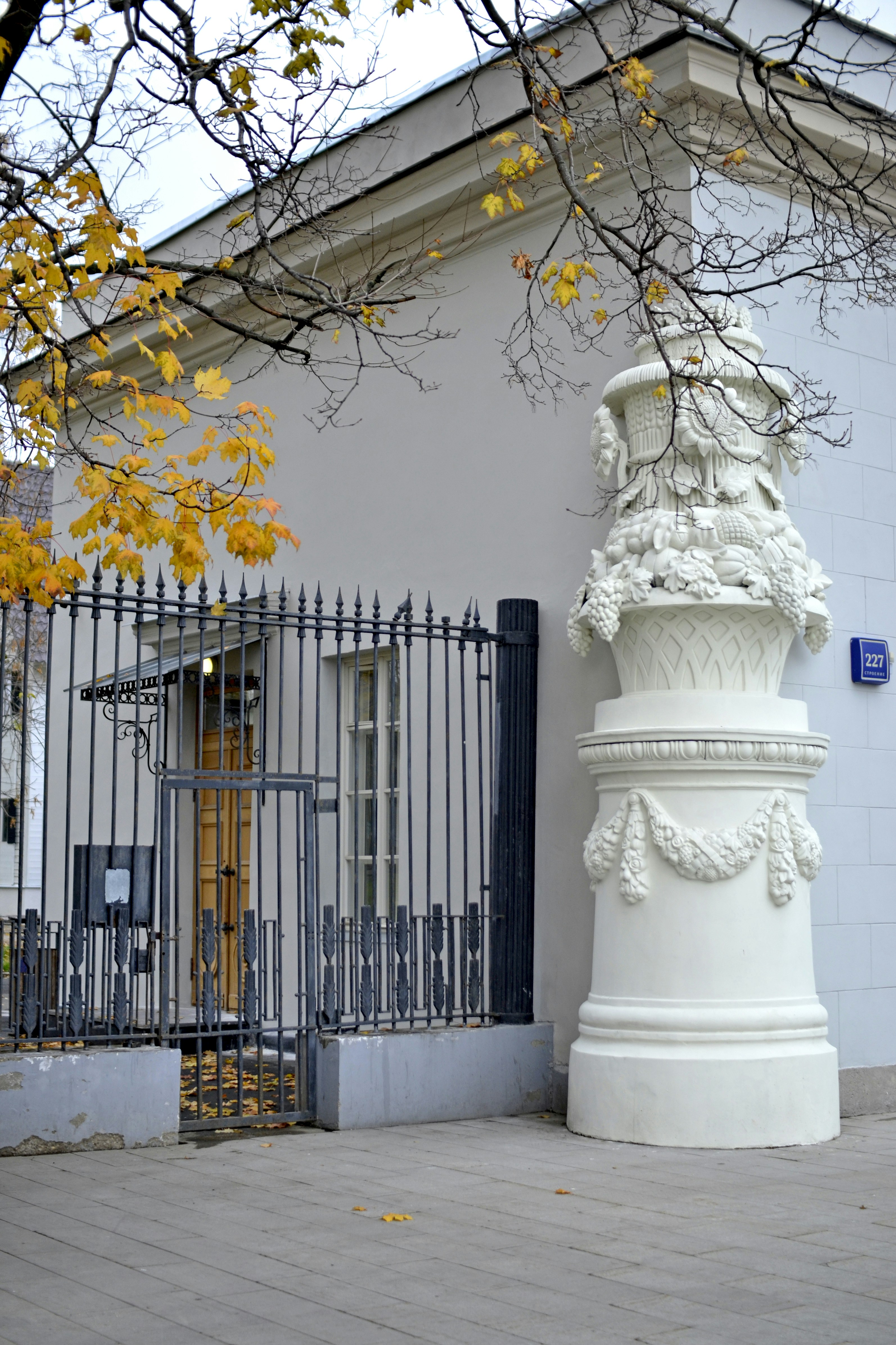 Carved Sentinel by the Gate: Autumn Leaves and Ironwork