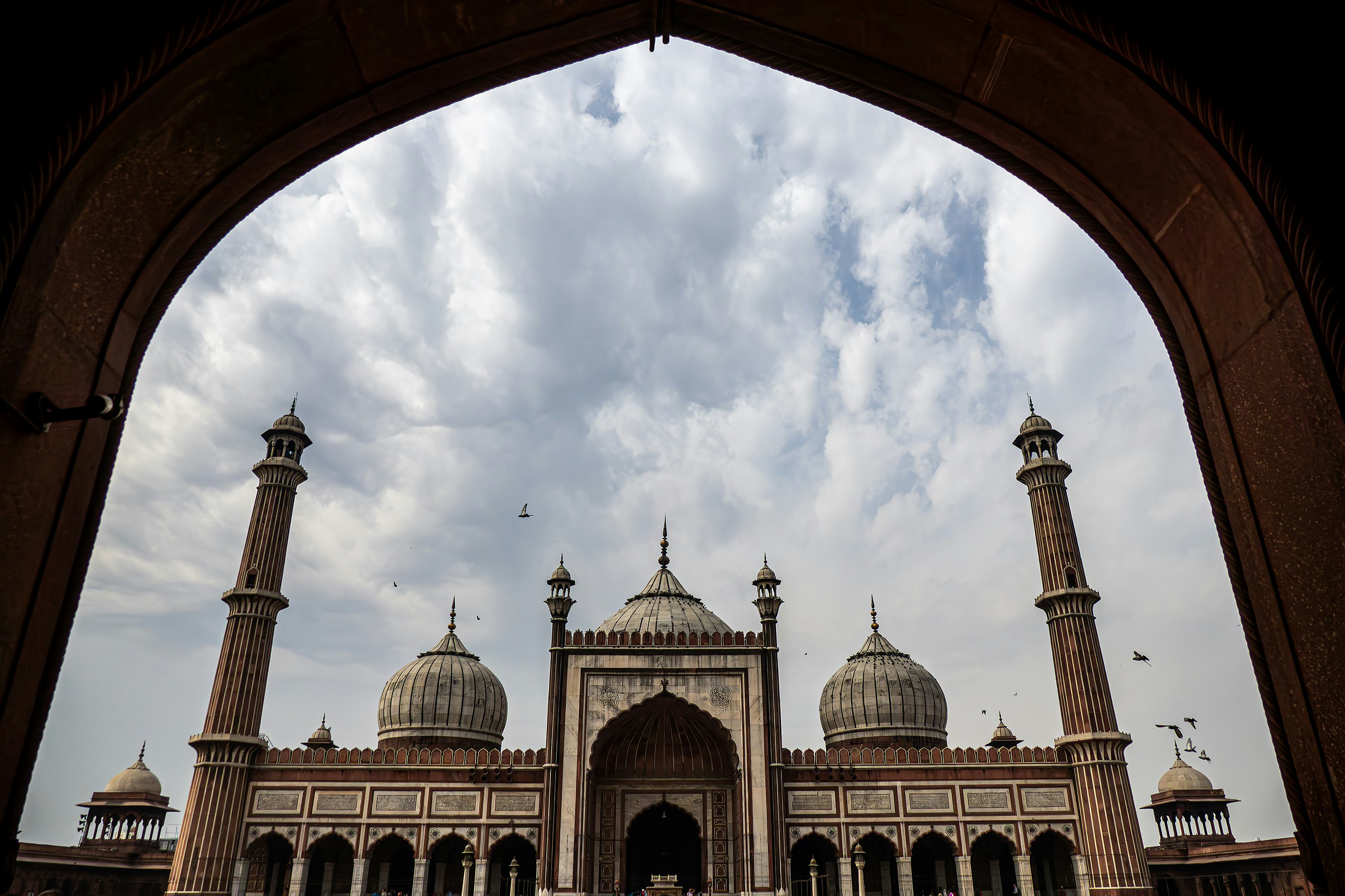 Jama Masjid's grand architecture viewed through an arched doorway under a dramatic sky.