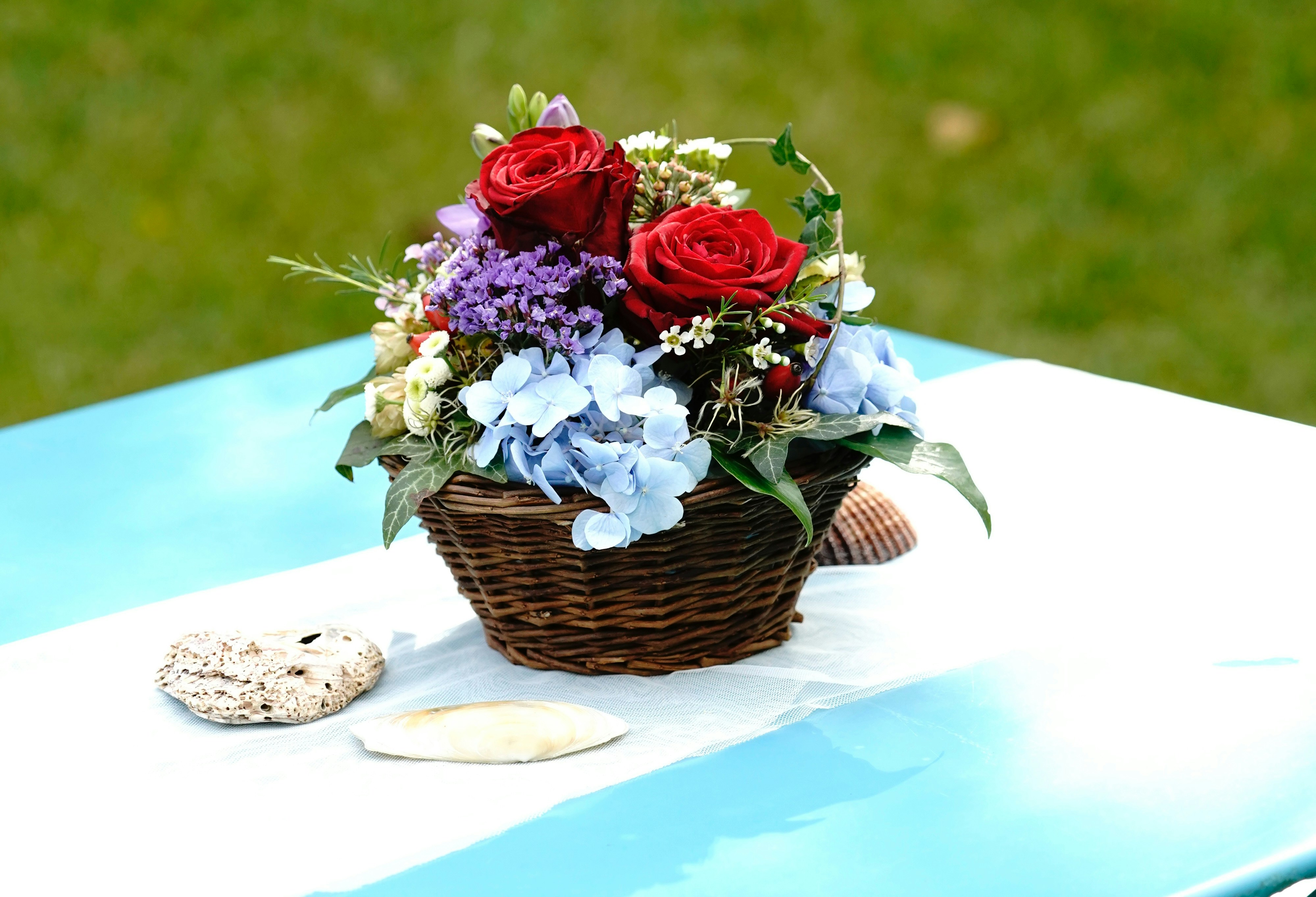 Sunlit Wicker Bouquet: Crimson Roses and Blue Hydrangeas on a Sky-Blue Table