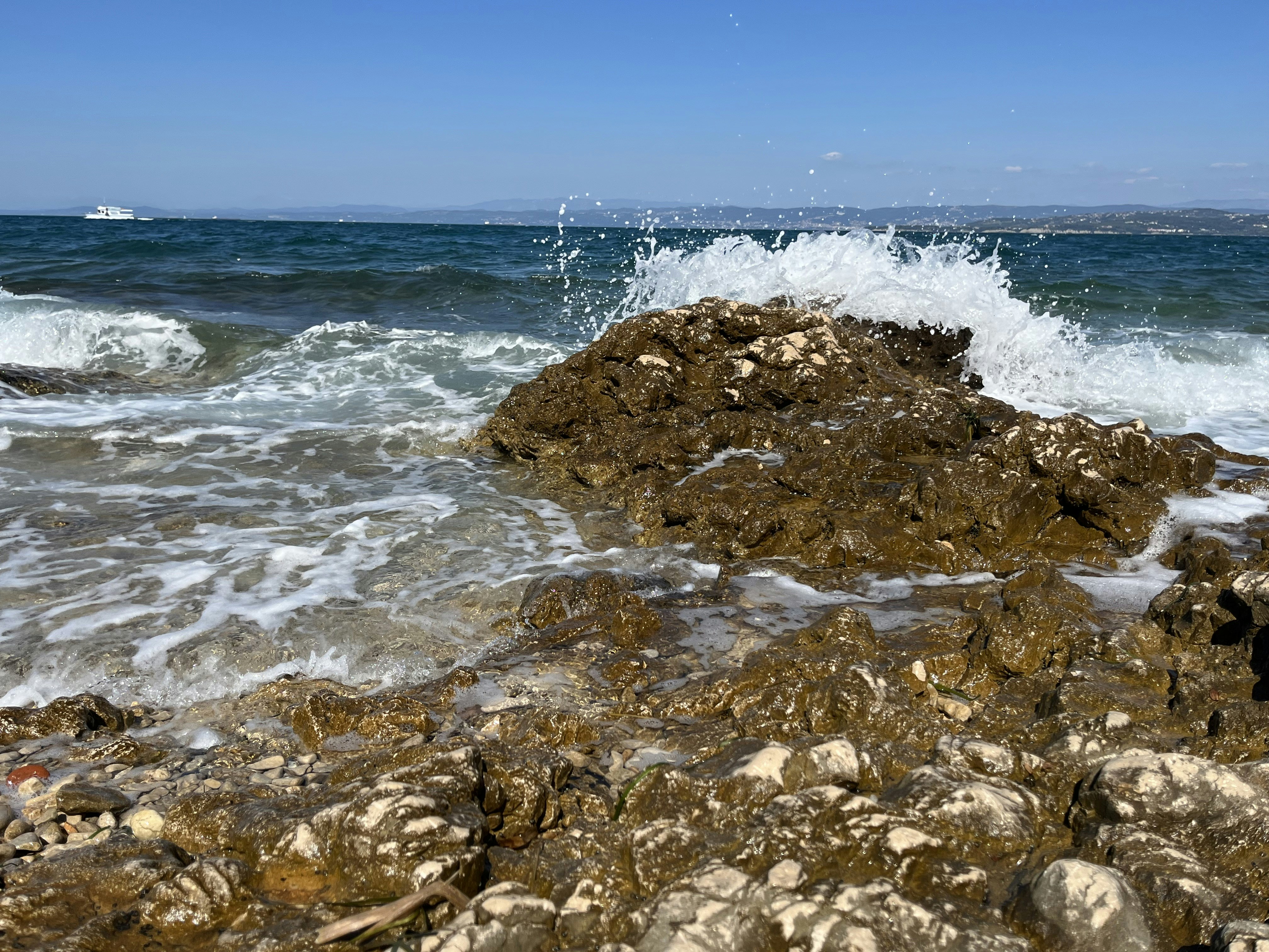 Rocky shoreline erupts with a curling wave under a clear sea breeze