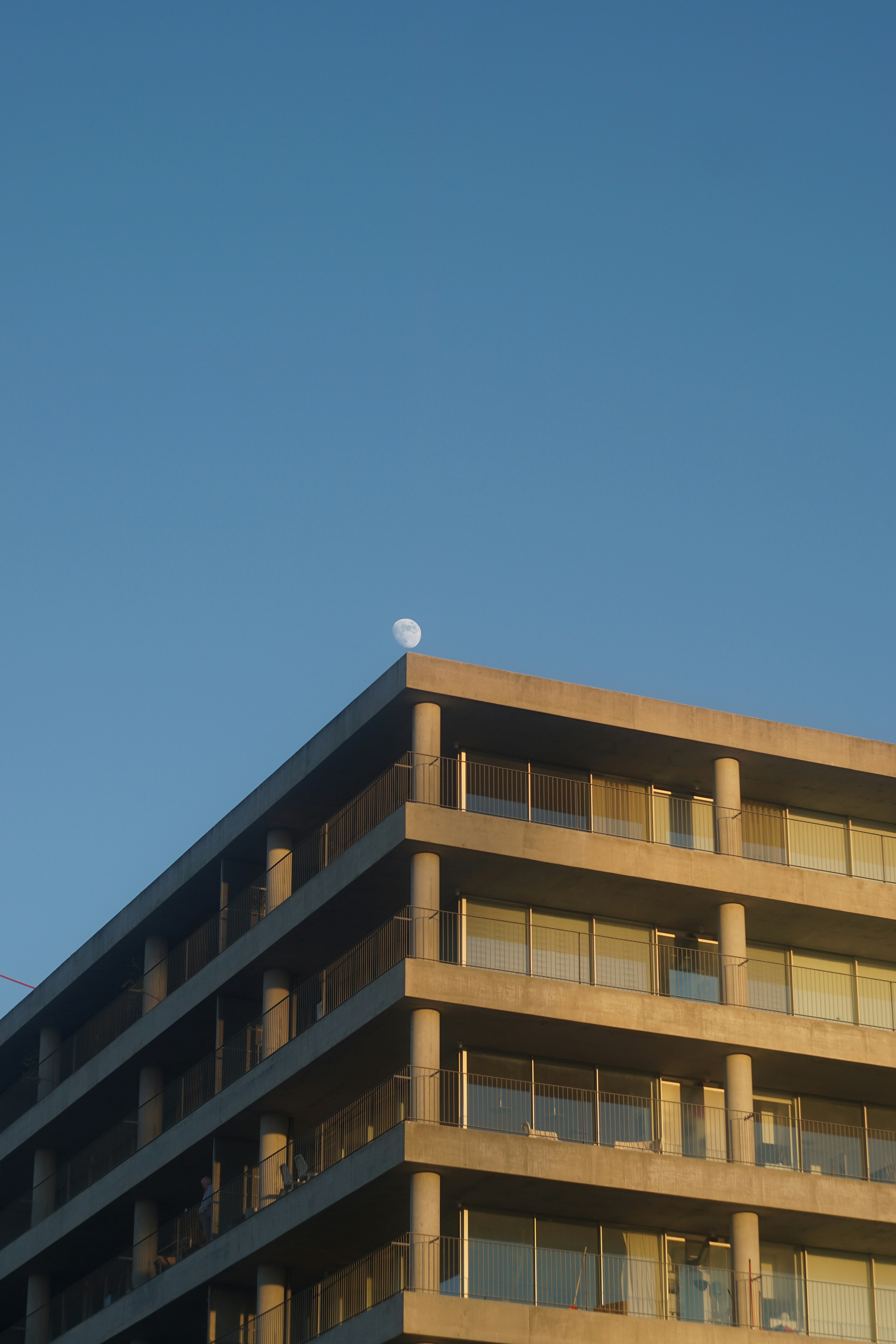 Moon Over the Braced Corners of a Sunlit Concrete Office Building