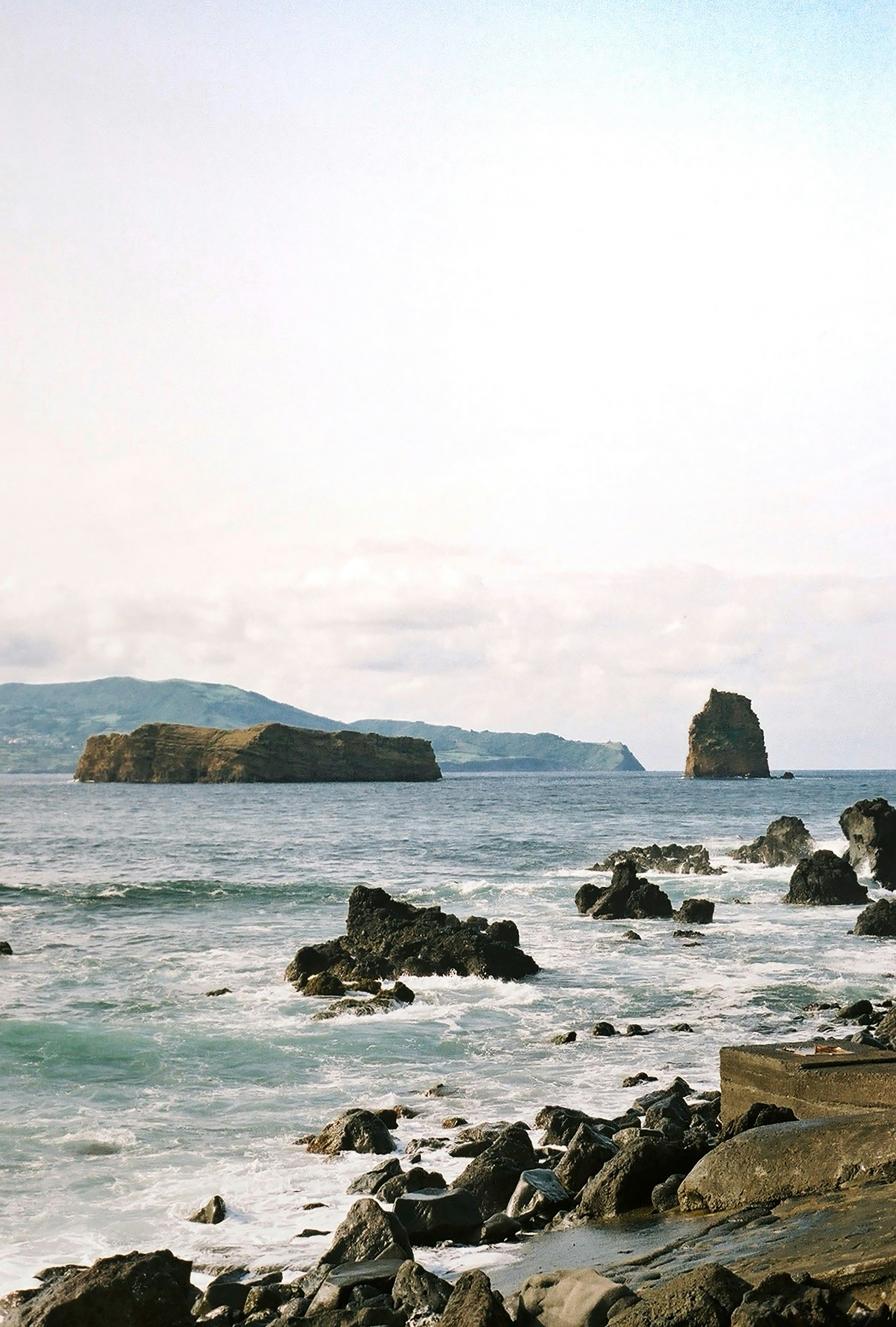 Rocky coastline with distant islands under a cloudy sky, showcasing the dynamic interplay of land and sea.