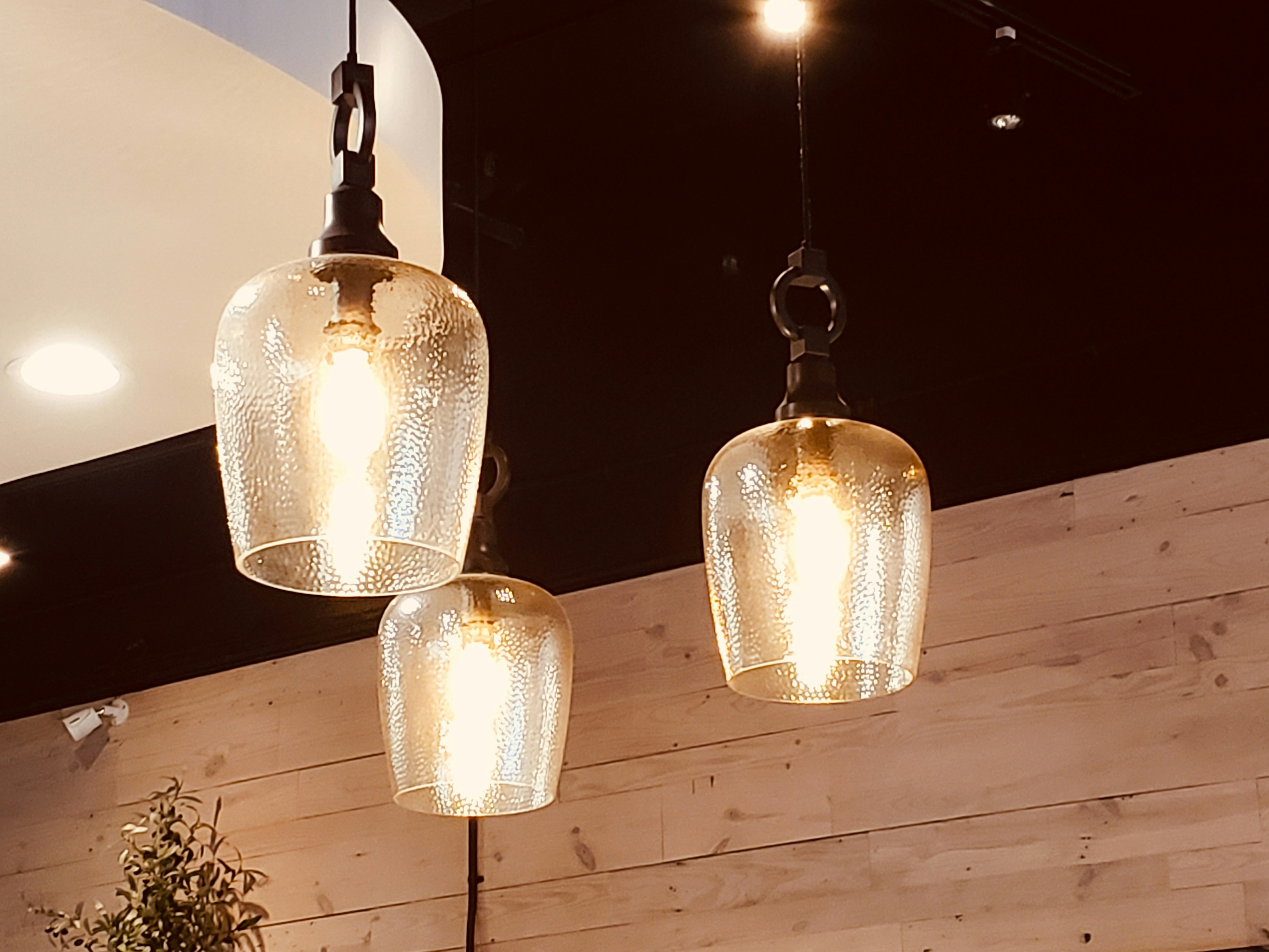 Three pendant lights with glowing bulbs hang against a wooden wall backdrop.