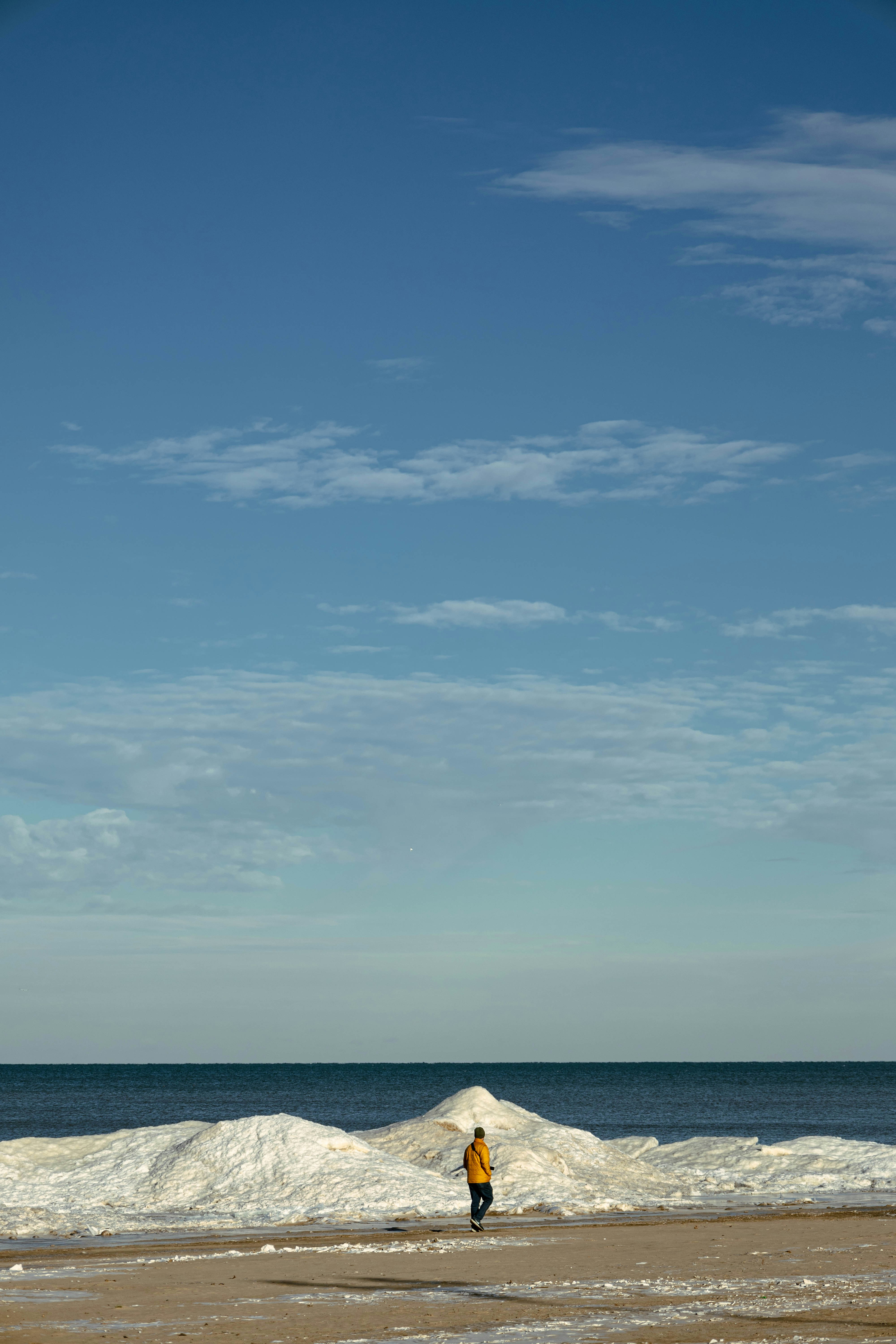 Orange on the Snow-Dusted Shore: A Lone Figure at Sea's Edge