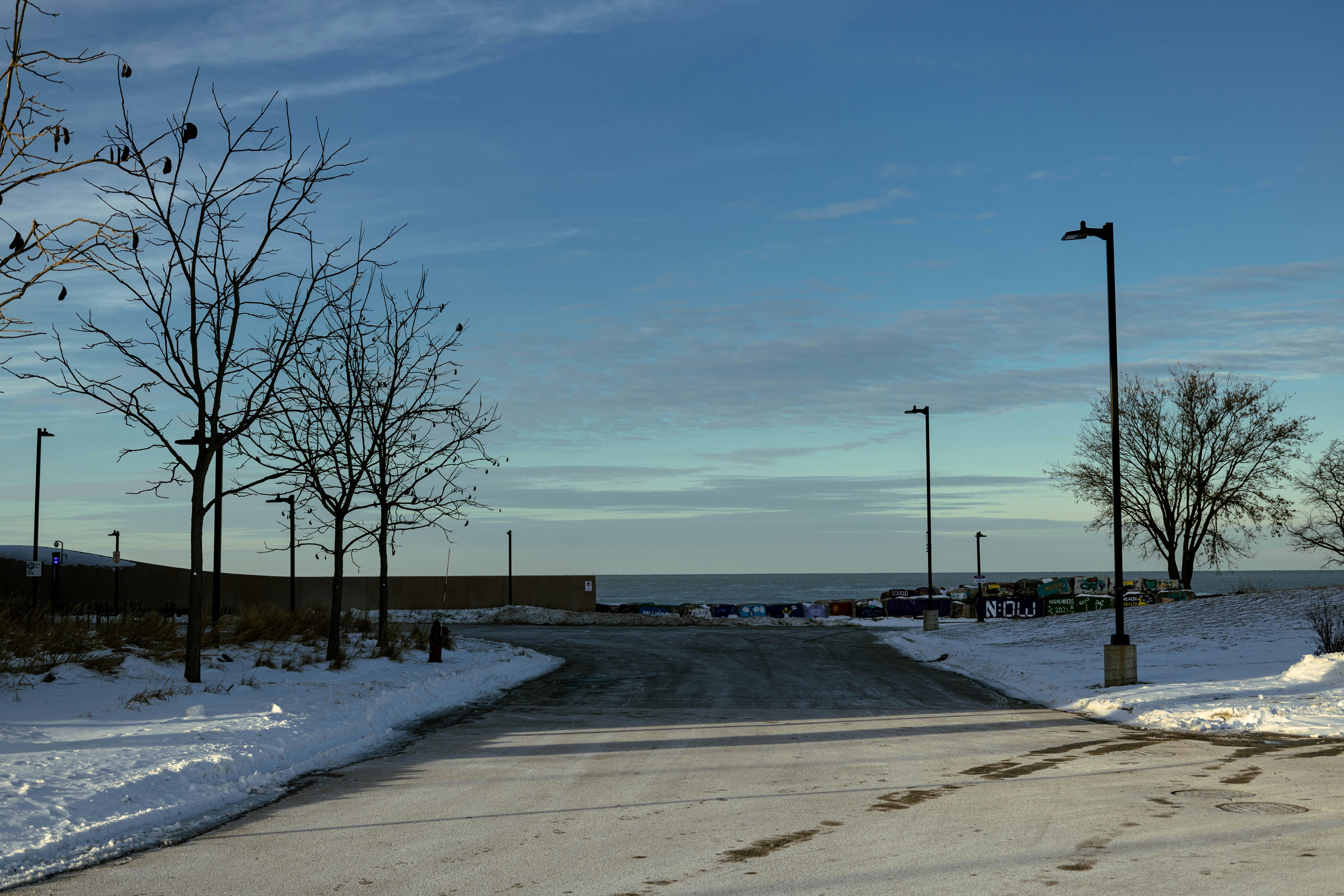 Snow-lined street leading to a serene waterfront under a clear blue sky.