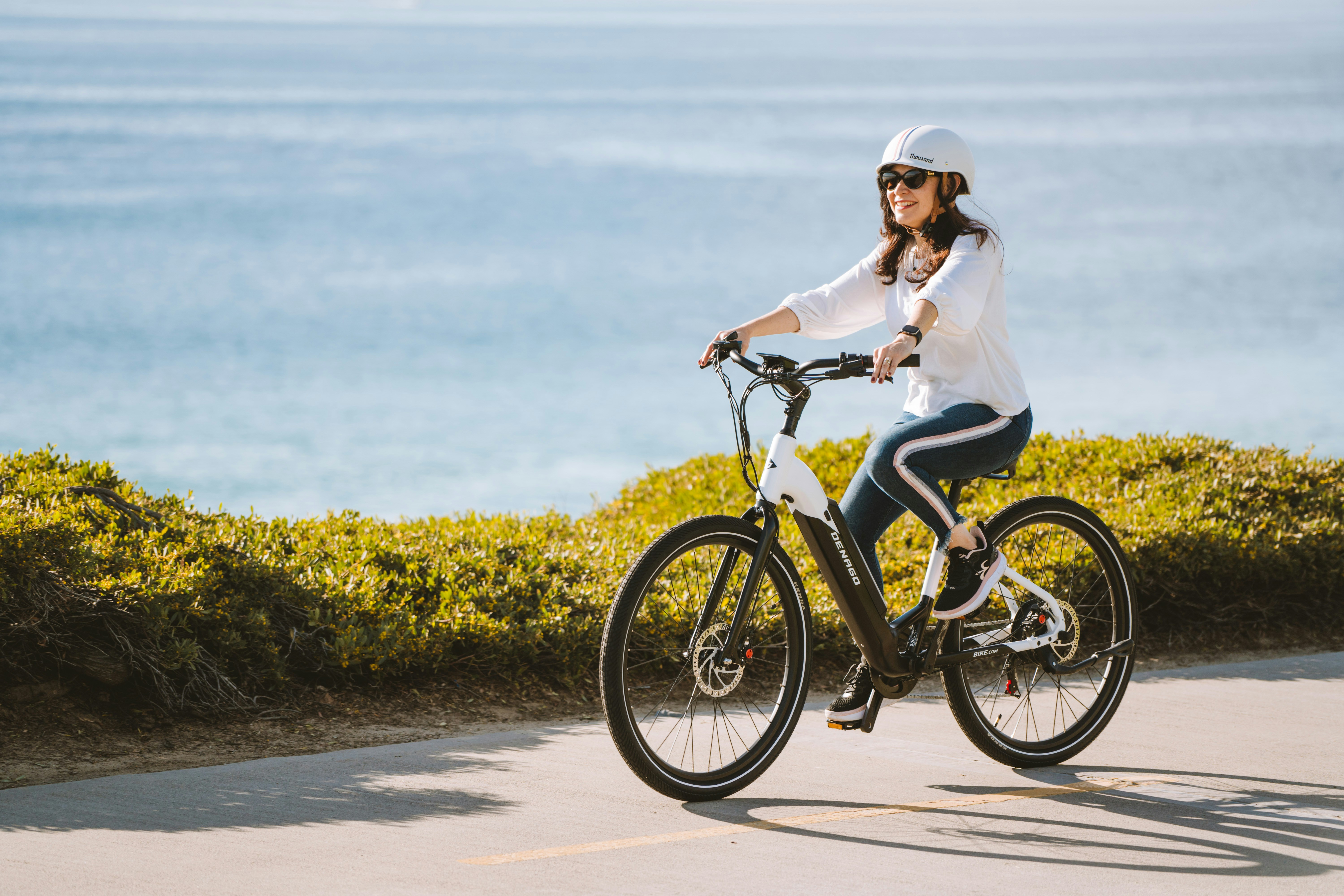 A woman riding a bike down a road next to the ocean photo – Free Girl ...