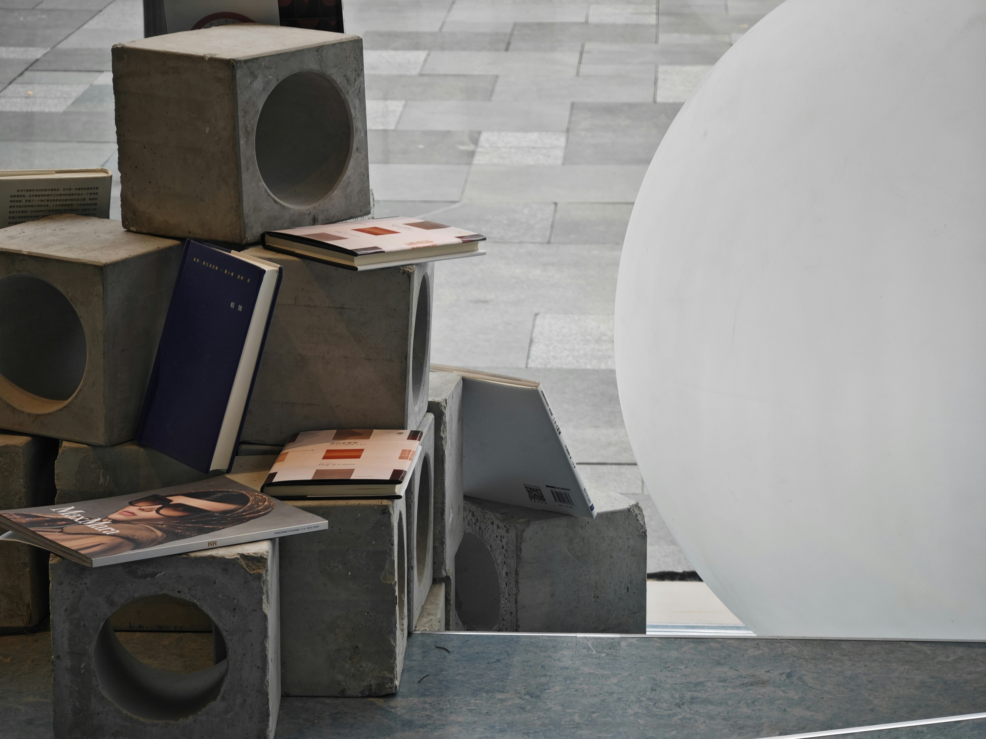 Books arranged on cement blocks beside a large white spherical structure indoors.