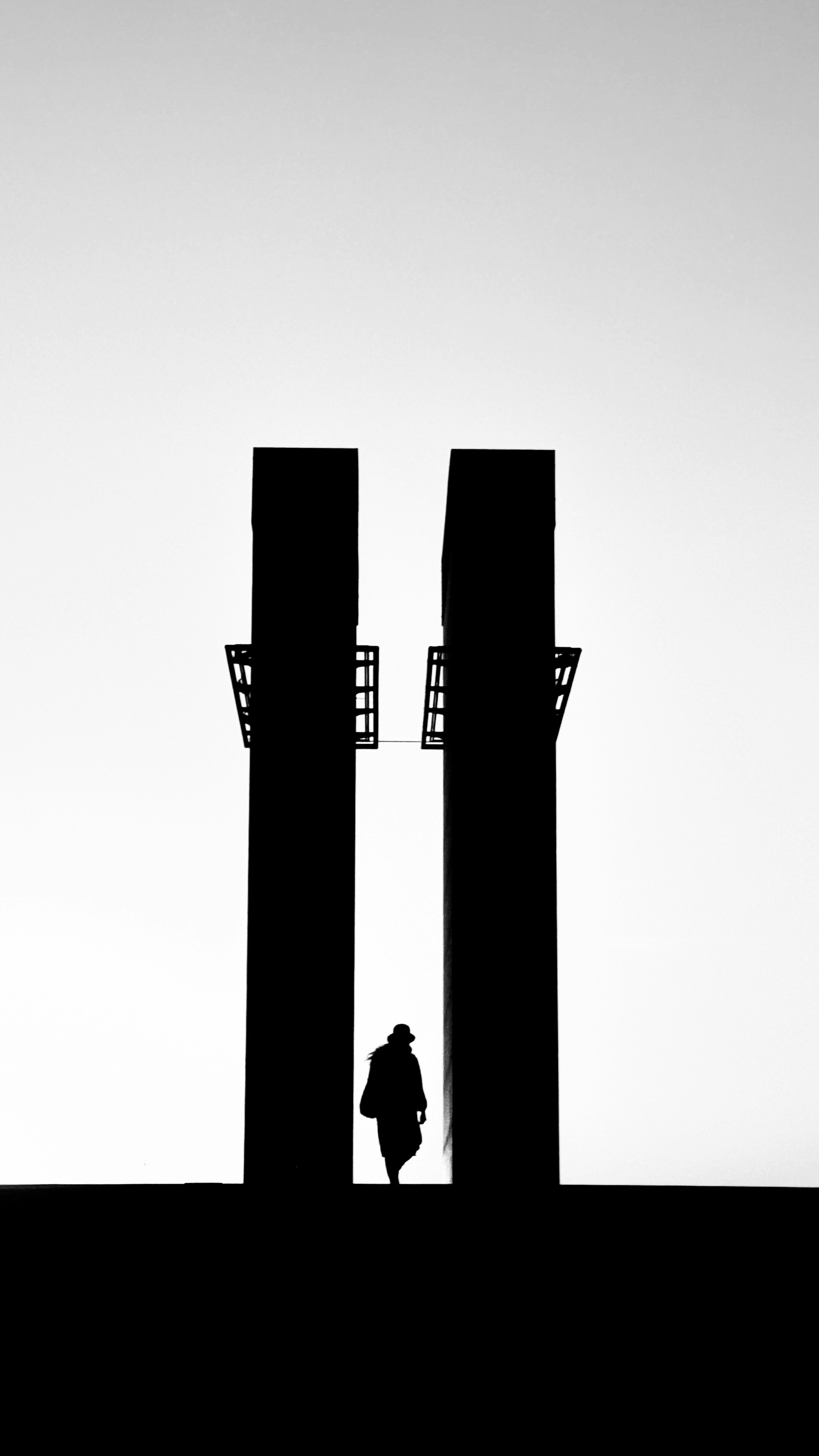 Lone Figure Between Twin Silhouettes Under a Pale Sky