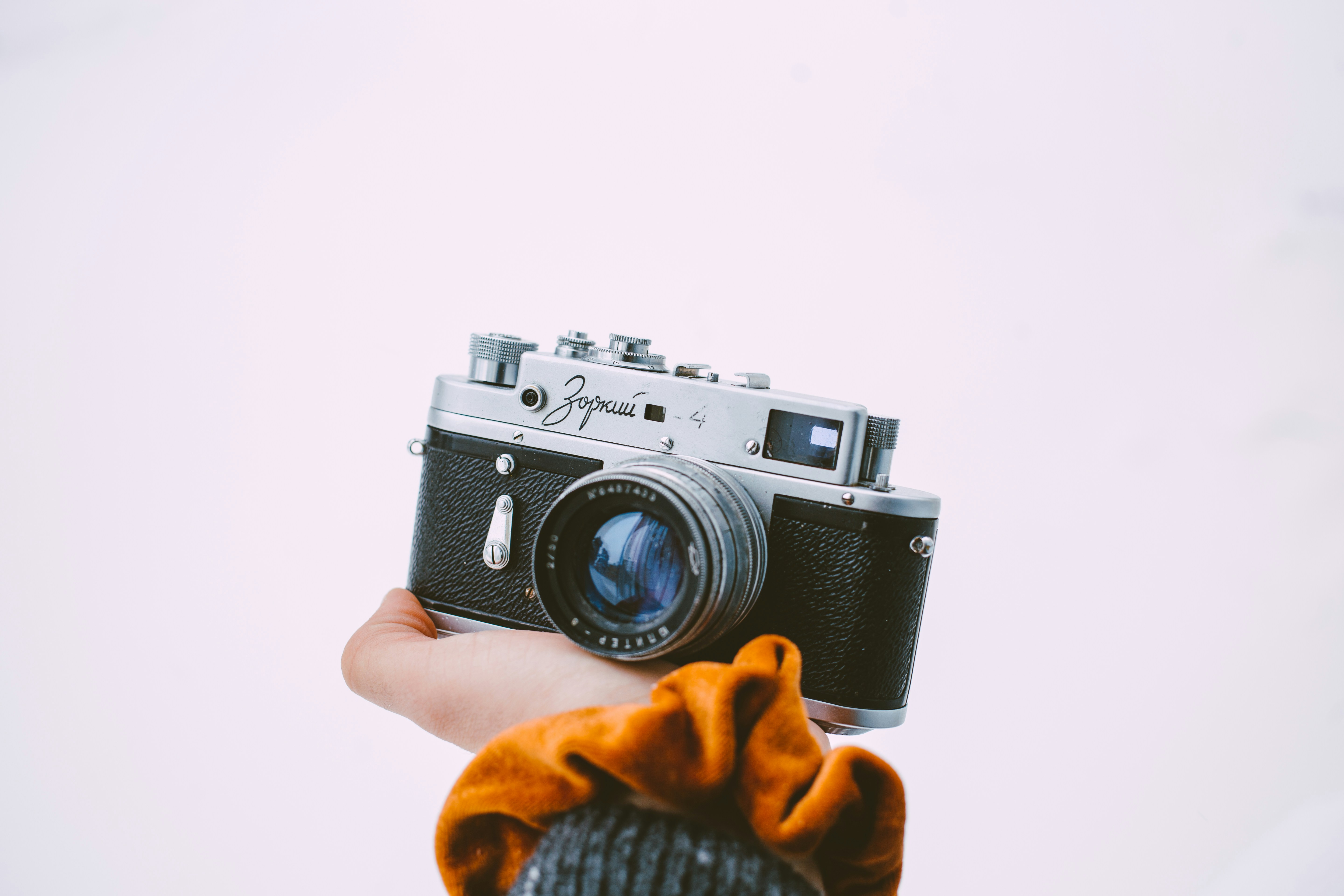 A vintage camera held by a person, showcasing its classic design and intricate details against a soft, blurred background.