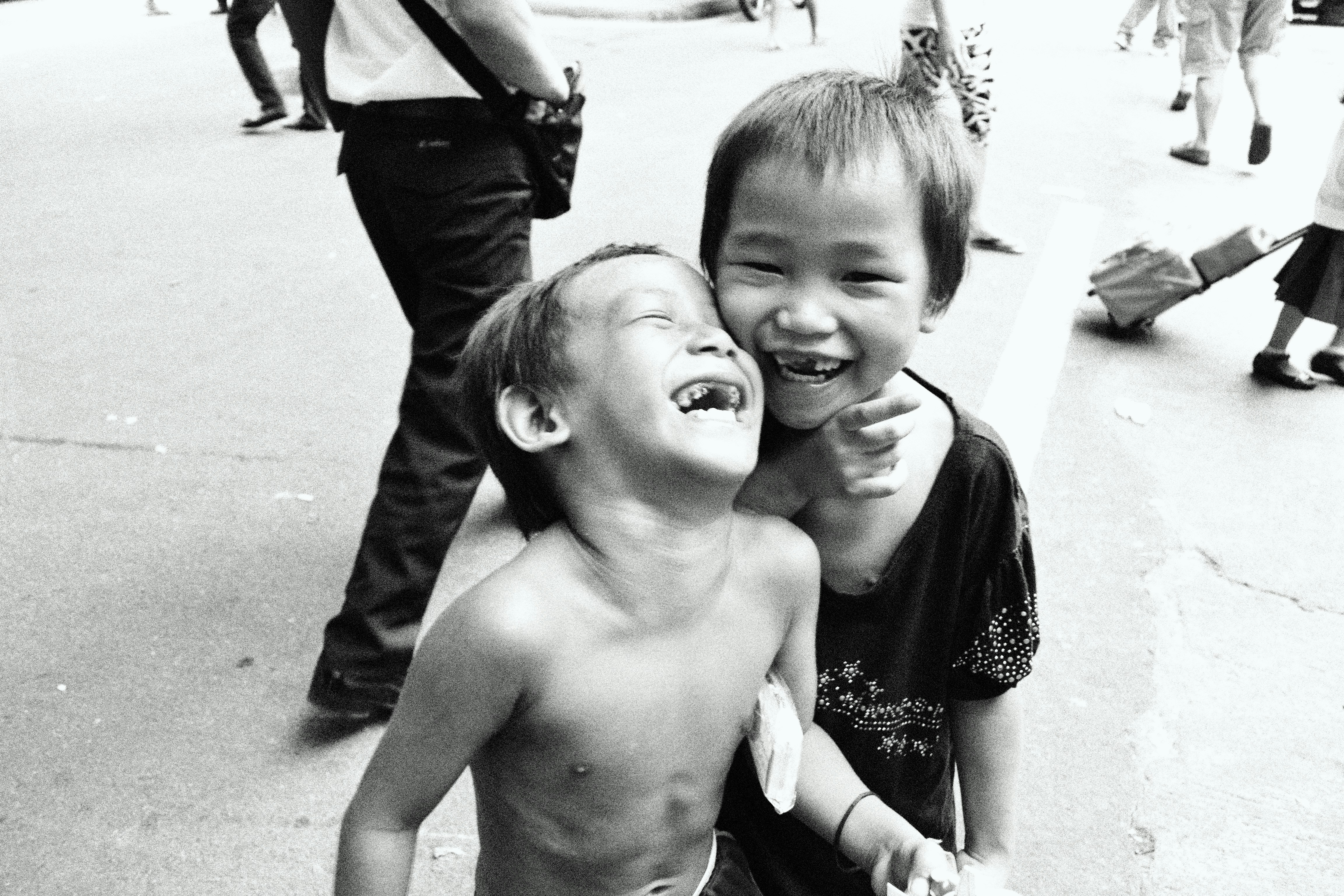 Two children share a moment of laughter amidst a busy street scene.