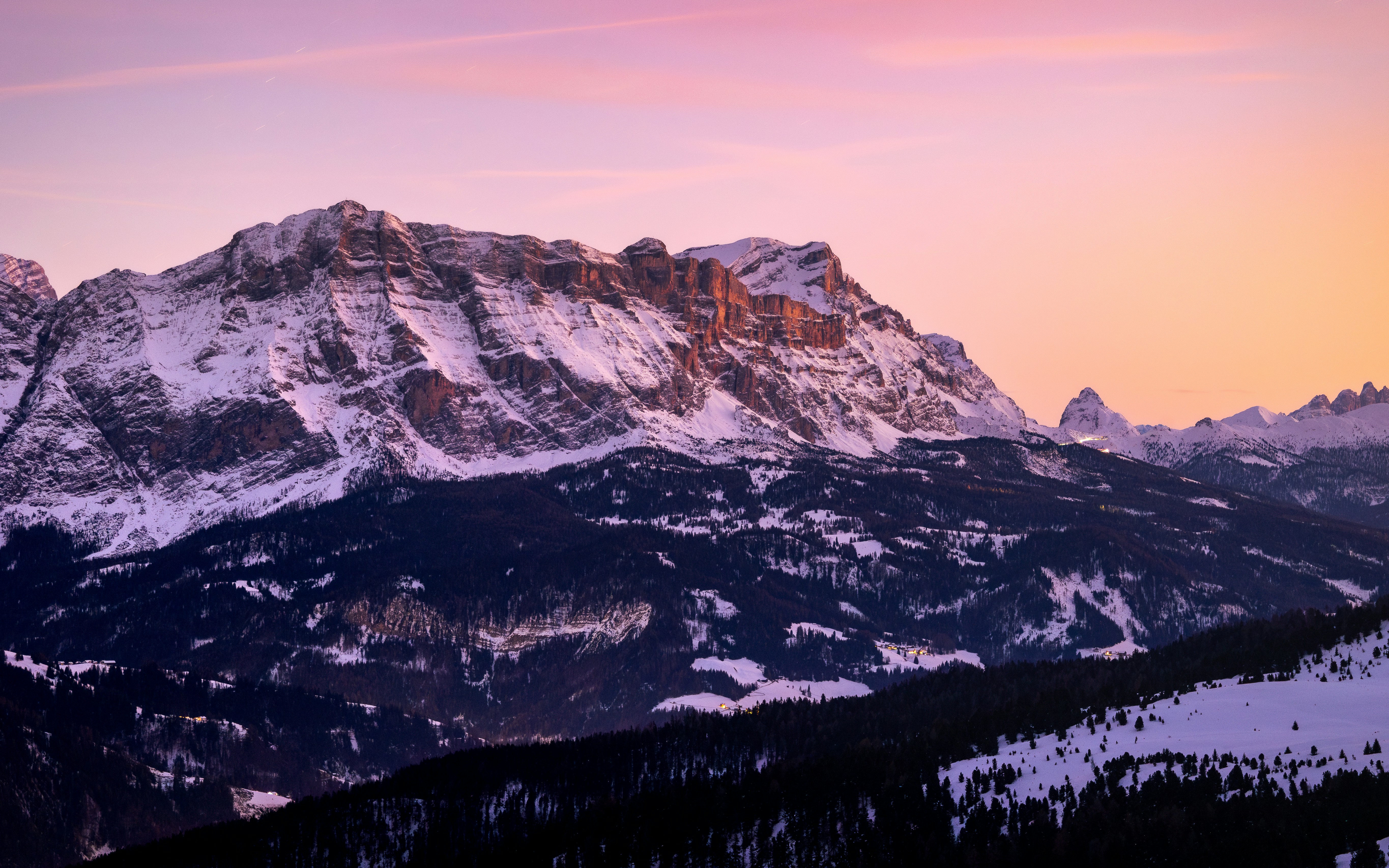 Snow-covered mountain range under a purple and pink sunset sky.