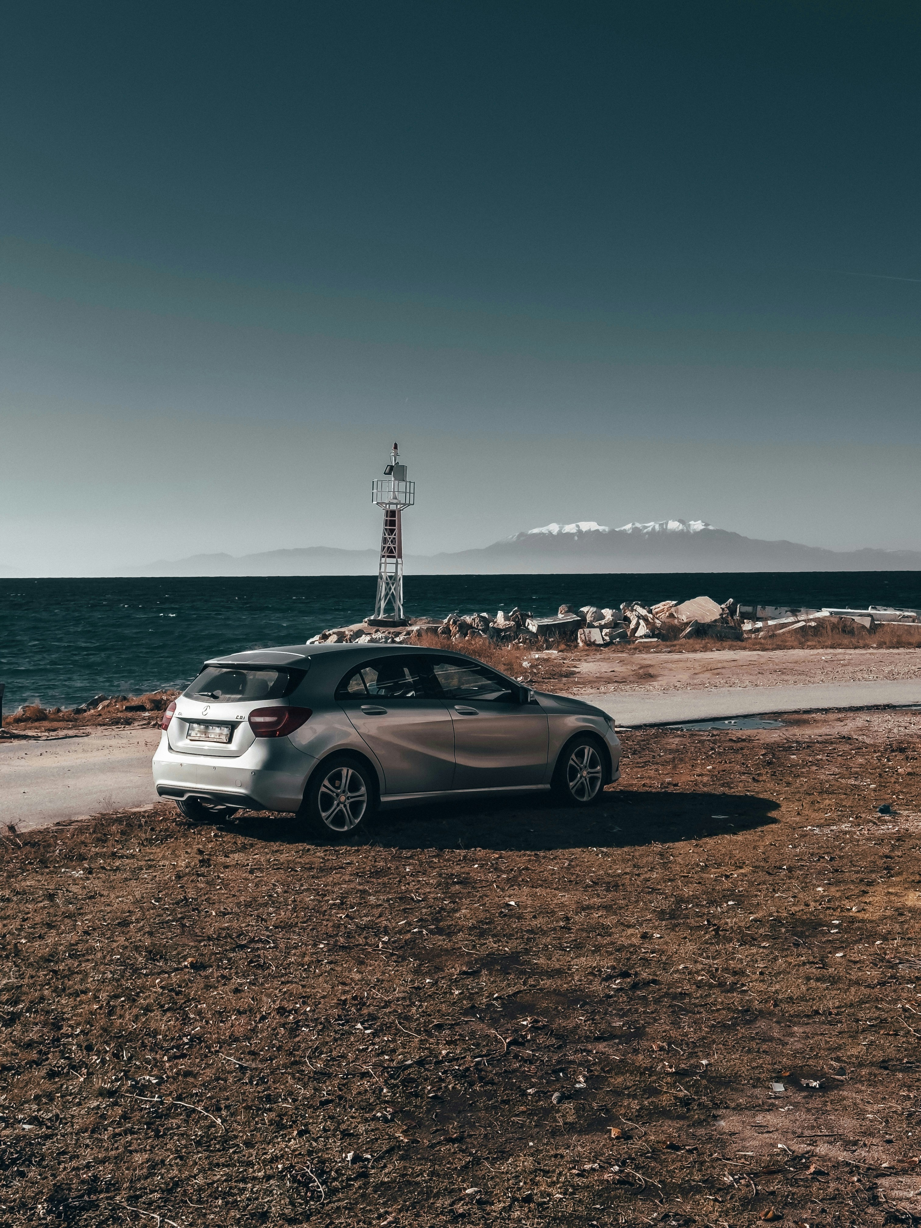 Coastal Quiet: Silver Hatchback by the Lighthouse