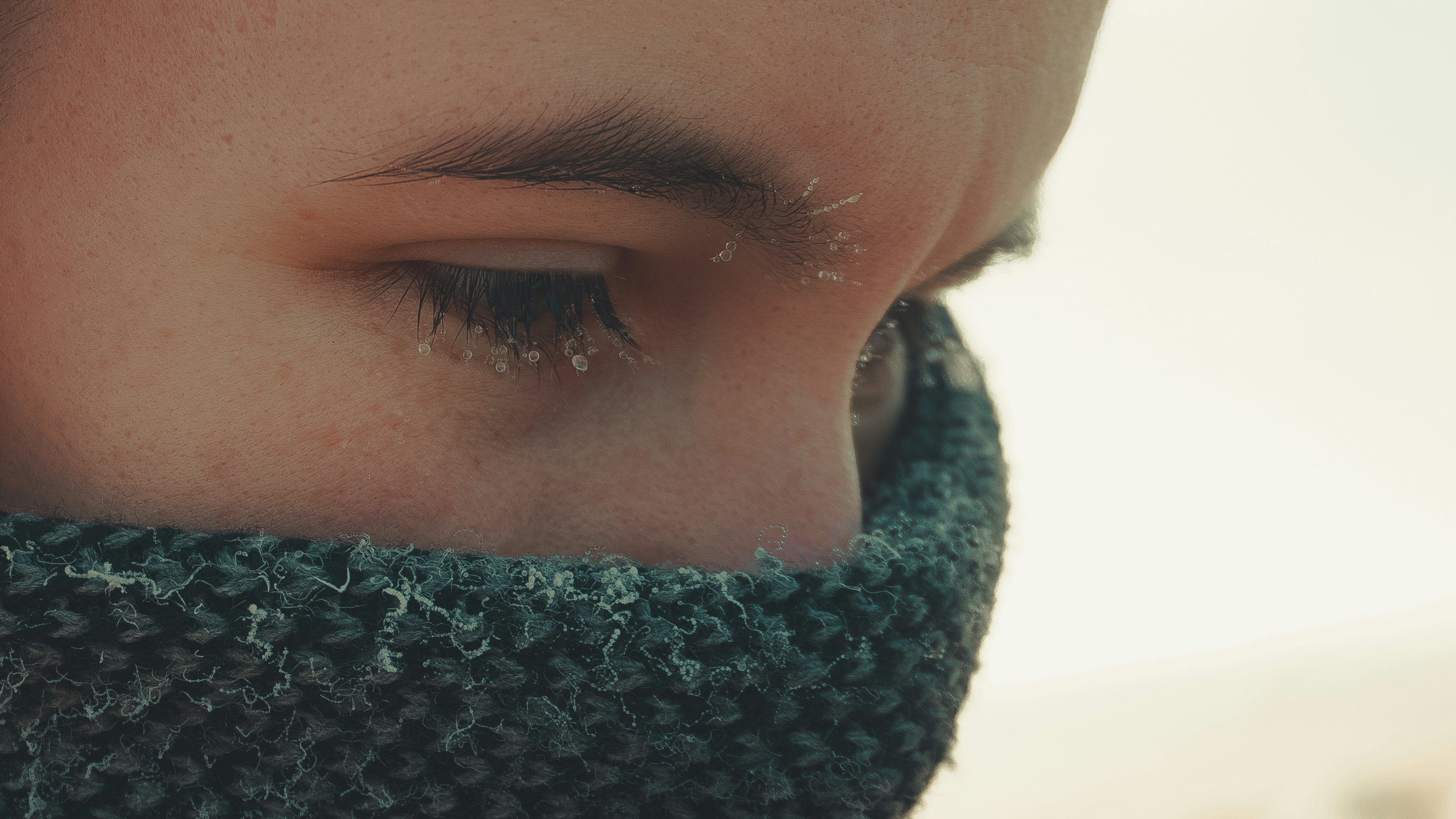 Close-up of a person's face with frost on their eyelashes, wrapped in a textured scarf, conveying a sense of cold and contemplation.