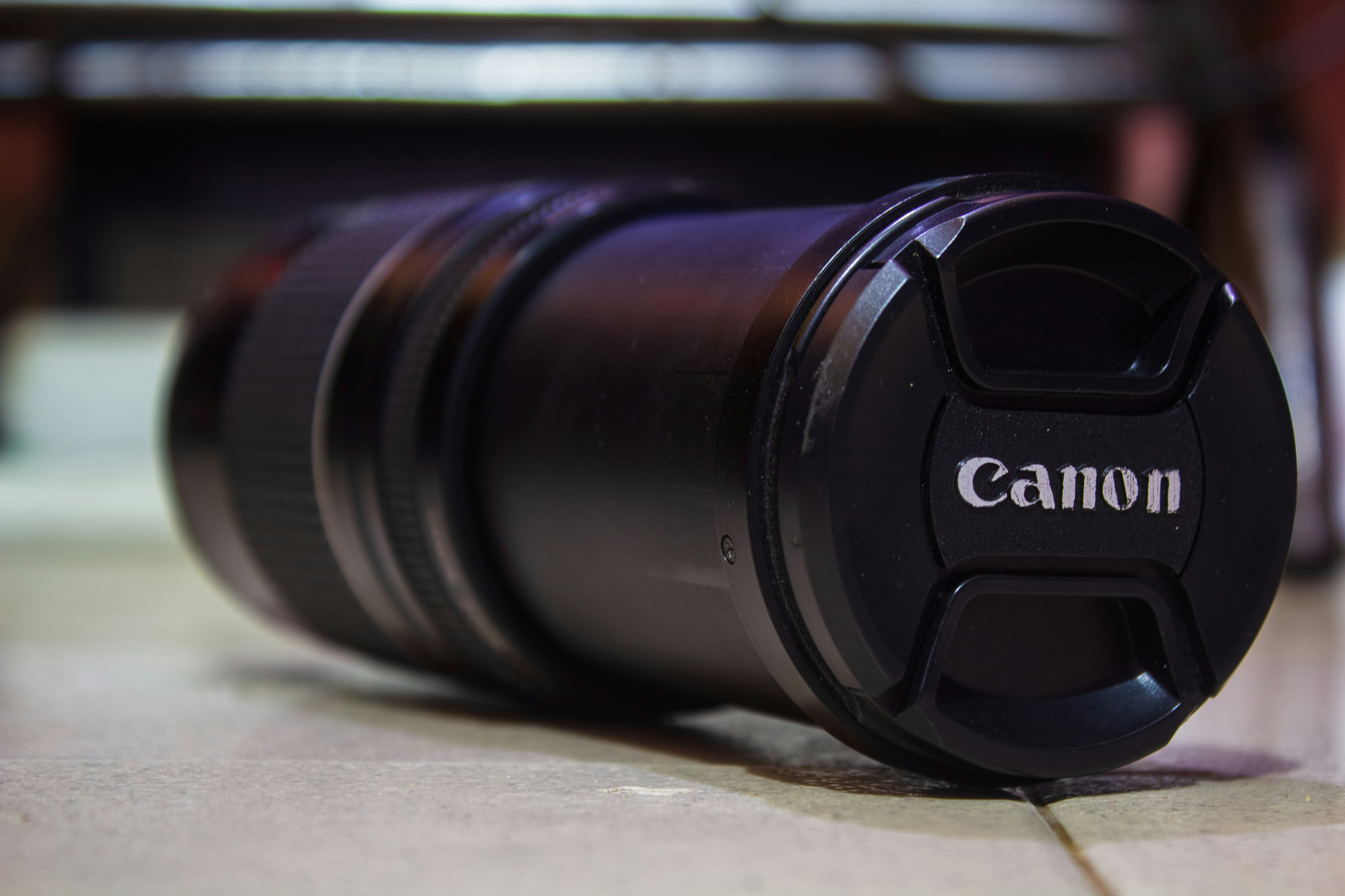 Closeup shot of a Canon 75-300mm telephoto lens. | a camera lens sitting on the ground next to a table