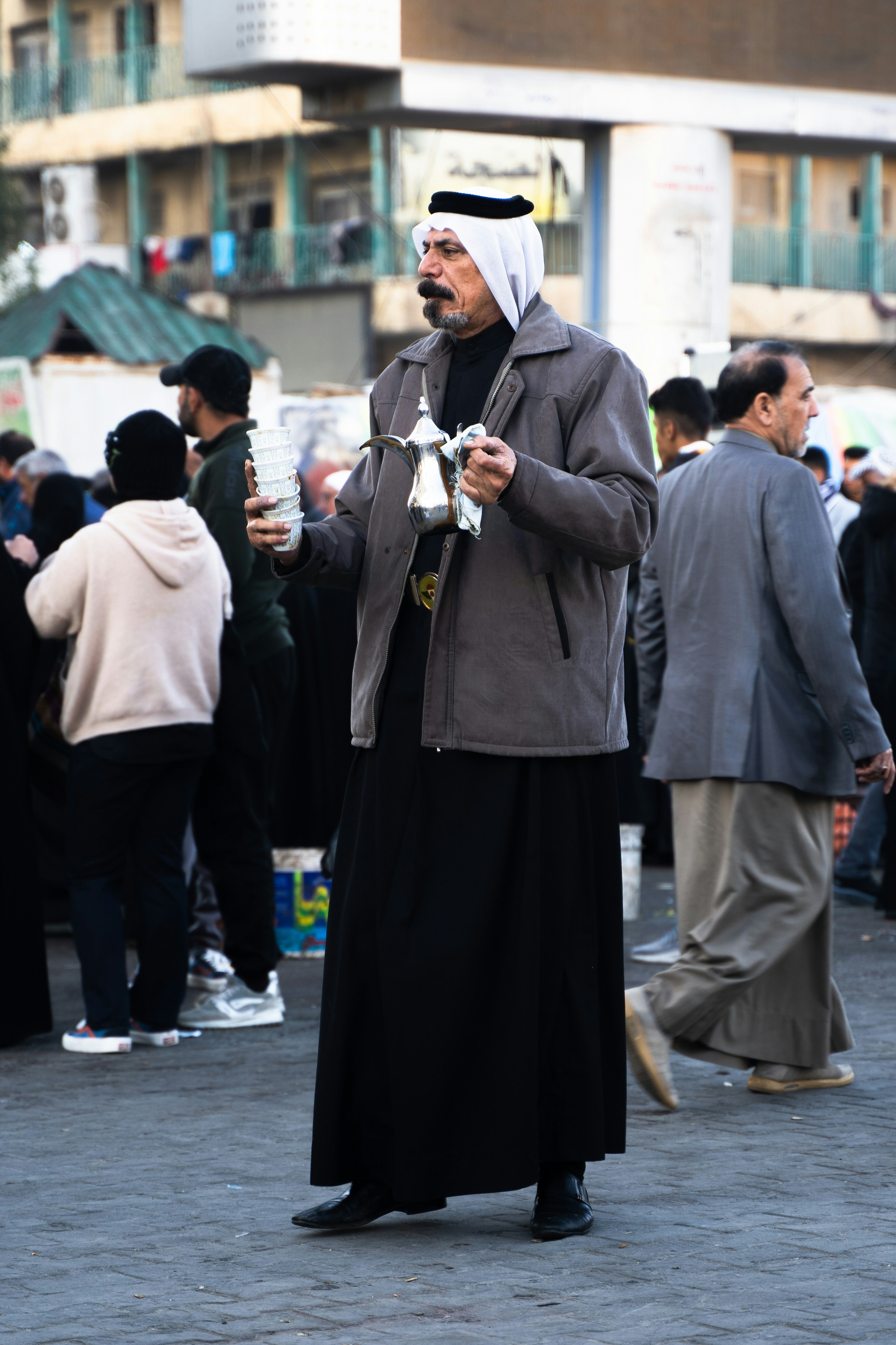 Market Portrait: A Traditional Coffee Vendor Amid a Bustling Crowd