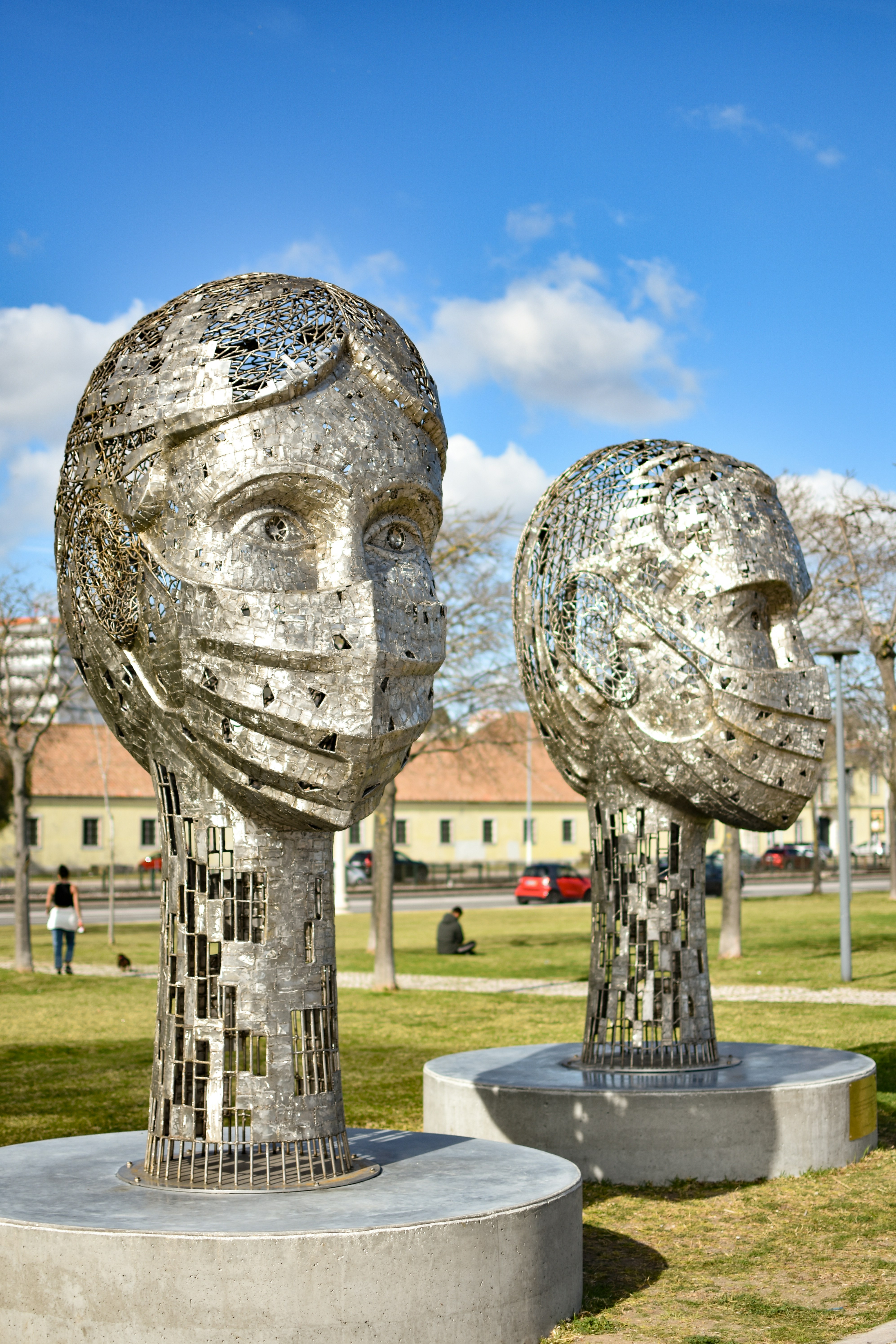 Metallic Heads in the Park: Sculpted Faces Against a Sunlit Sky