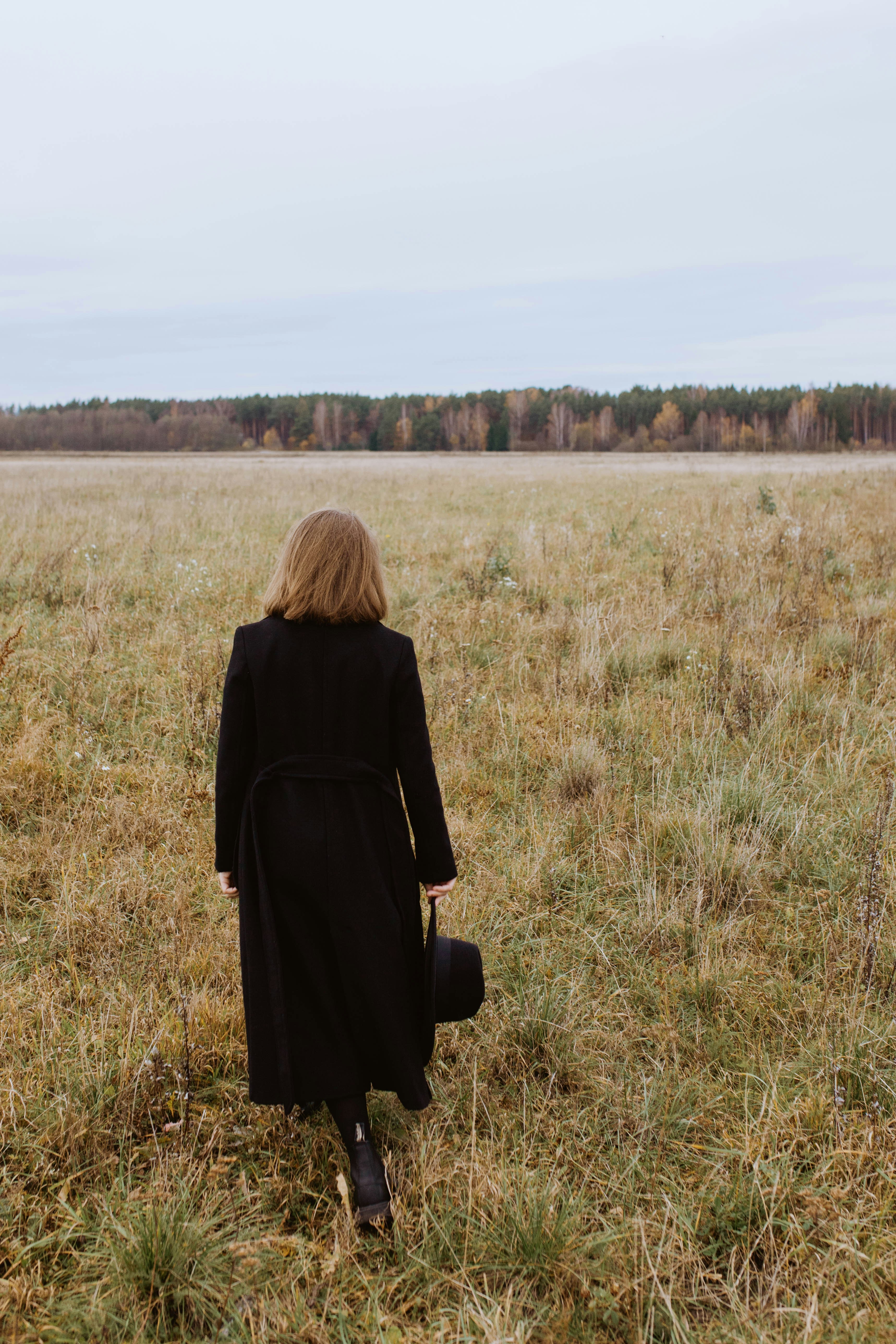 Exit from the Field: A Woman in Black Walks Toward the Tree Line