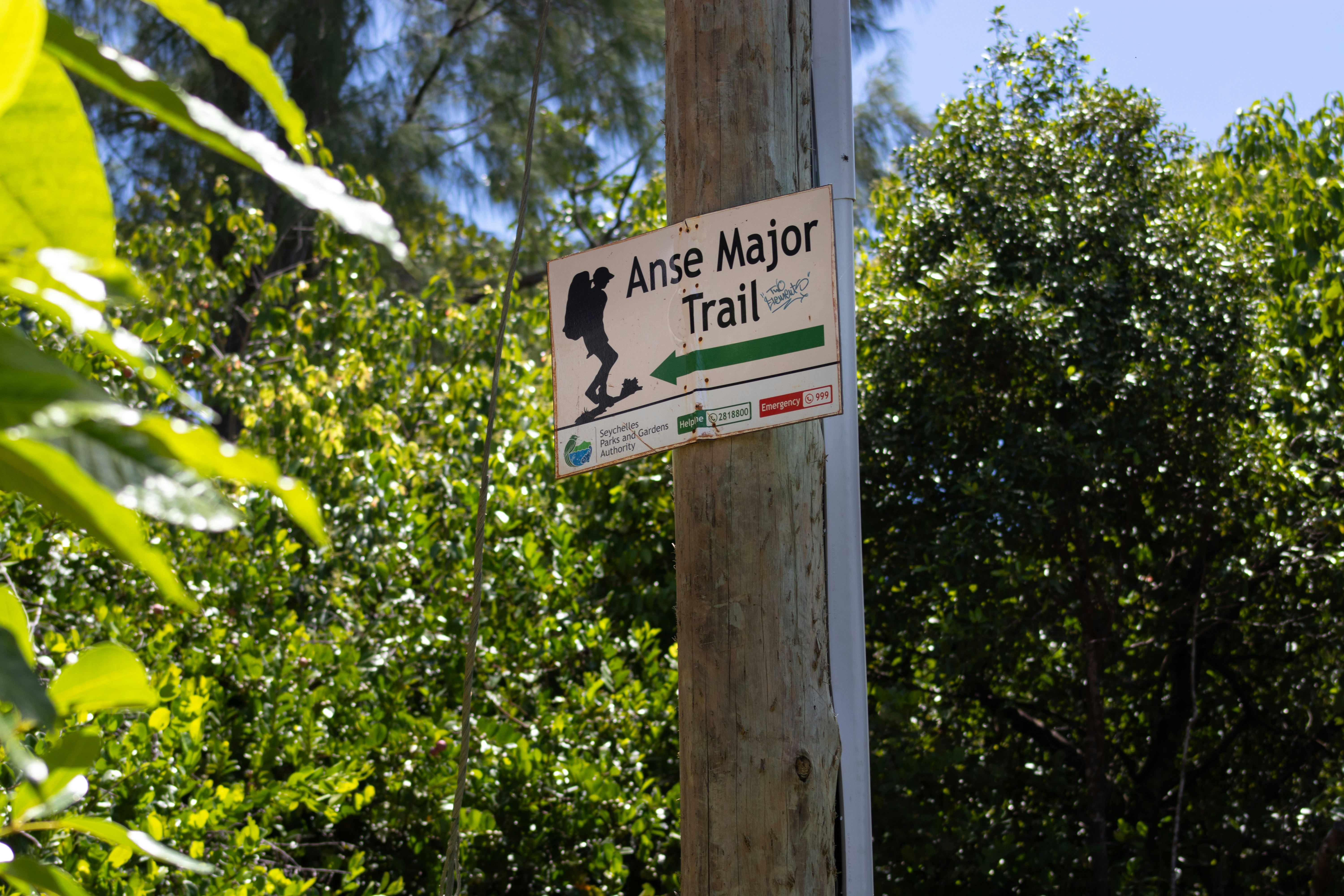Trail signpost for Anse Major surrounded by lush foliage under a clear blue sky.