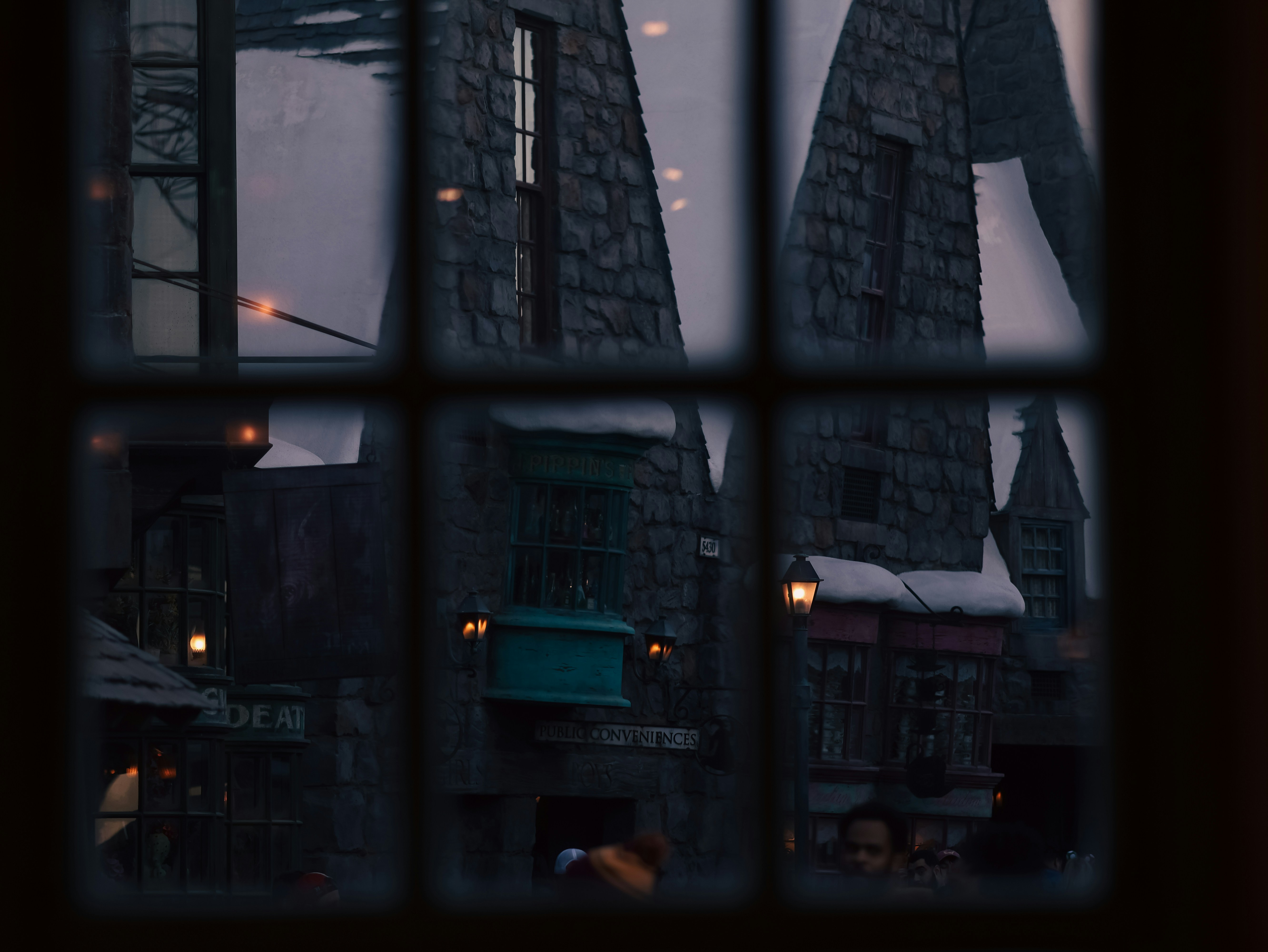 Snow-covered rooftops and stone buildings seen through a window frame at dusk.