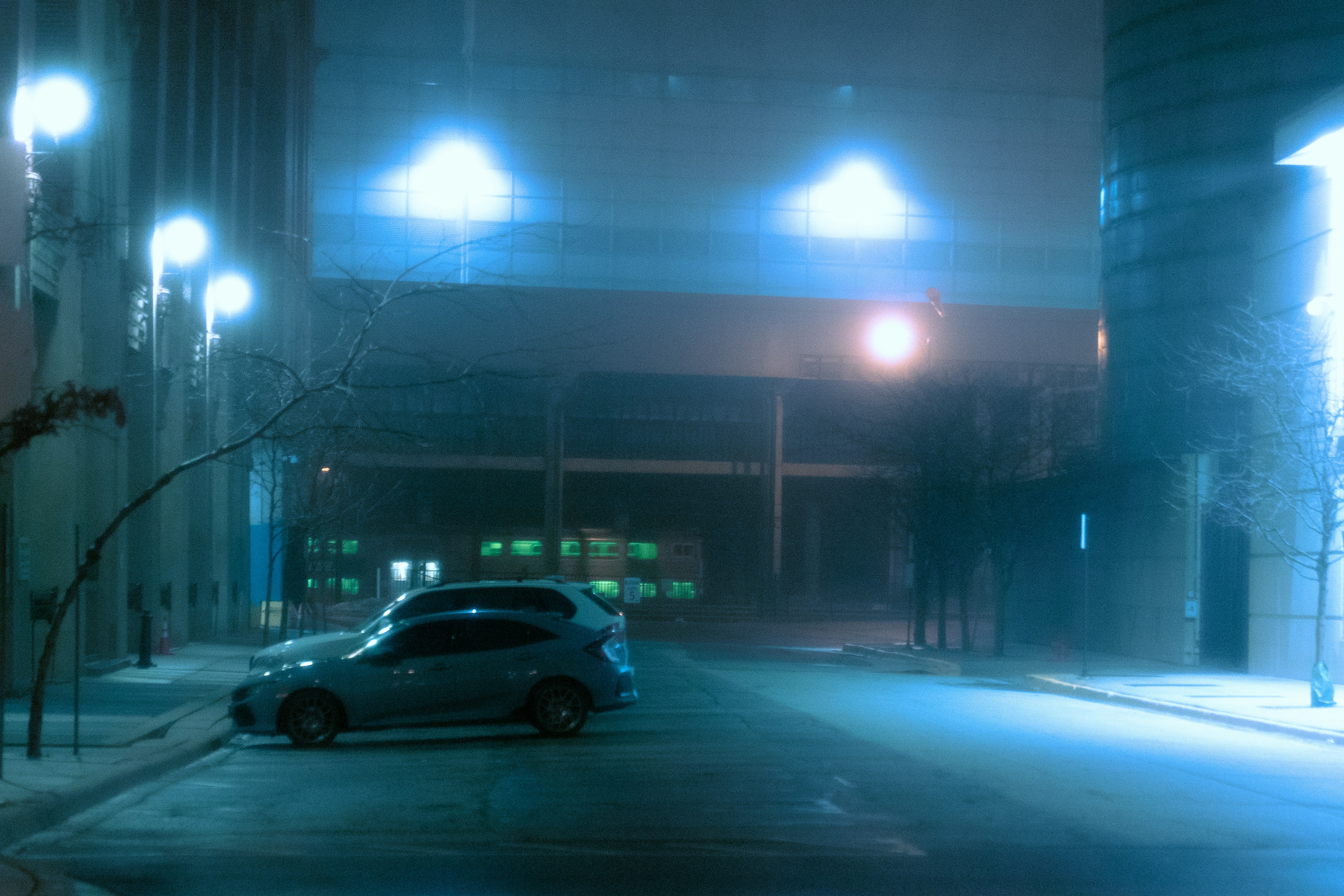 Car parked on a dimly lit urban street enveloped in fog, with tall buildings framing the scene.