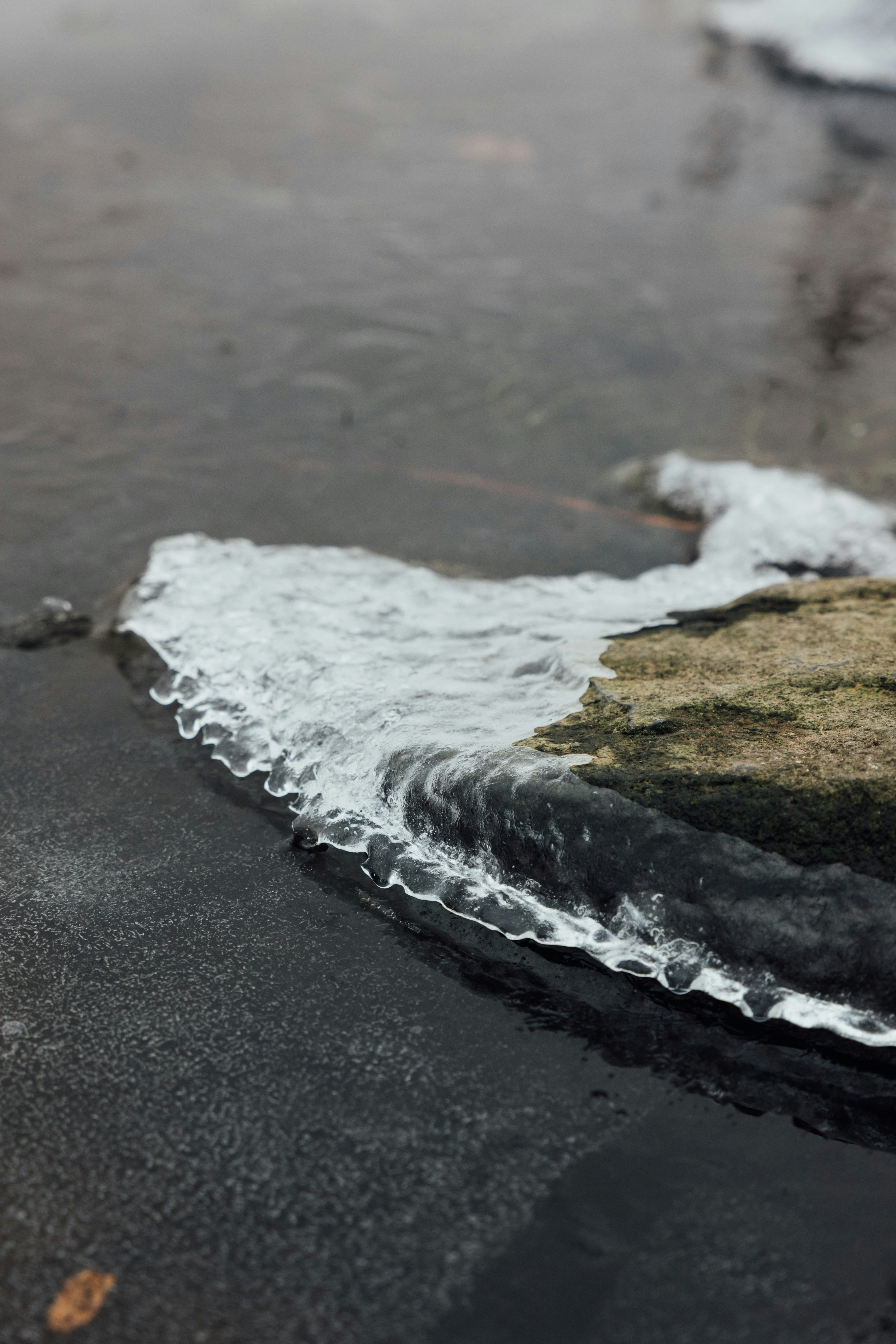 Close-up photograph of a curling white foam wave along dark sand, with a rocky outcrop in the foreground.