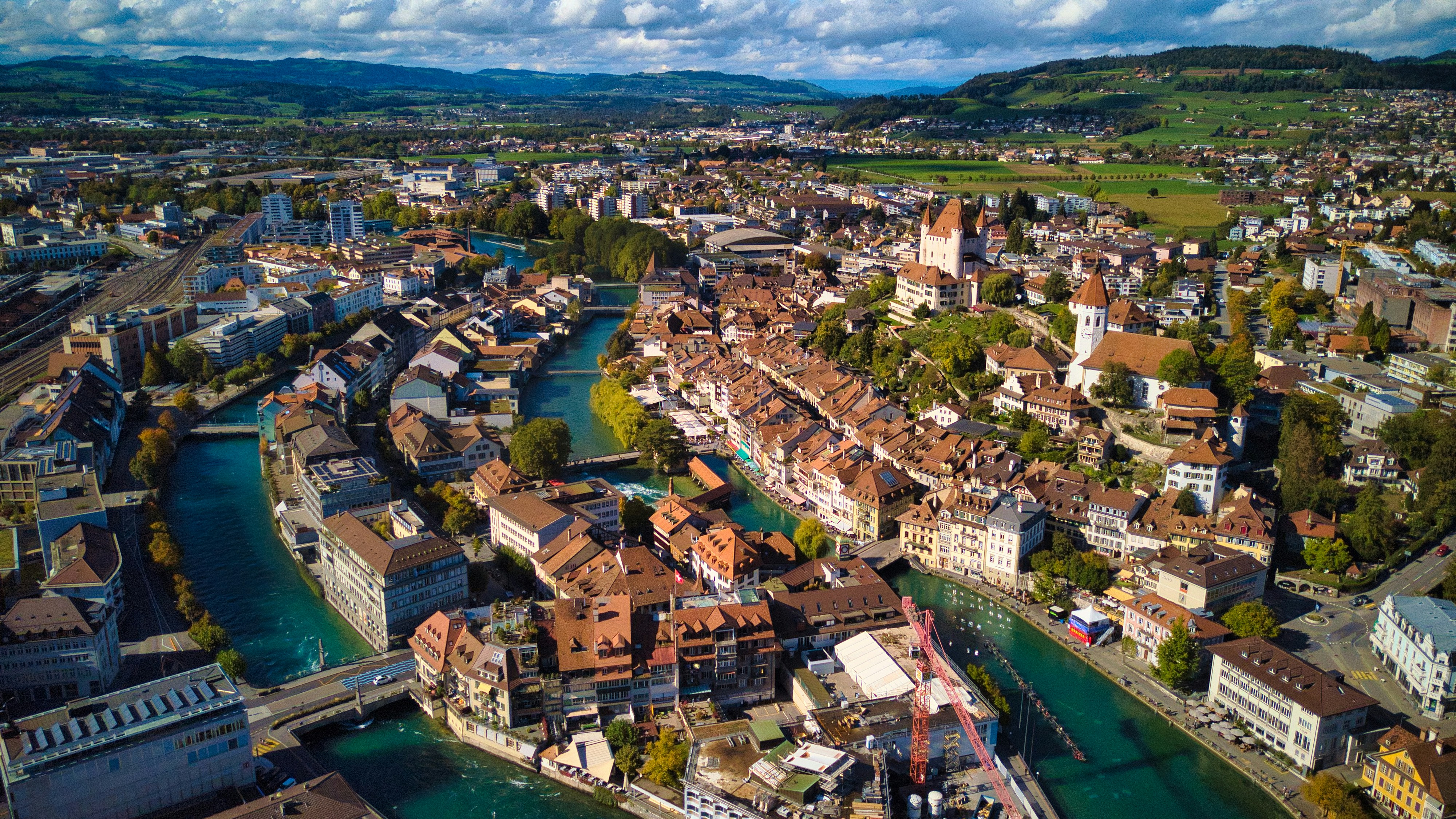 Charming riverside town with historic architecture and lush green hills, captured from above. The scene showcases the interplay between urban development and natural landscapes.