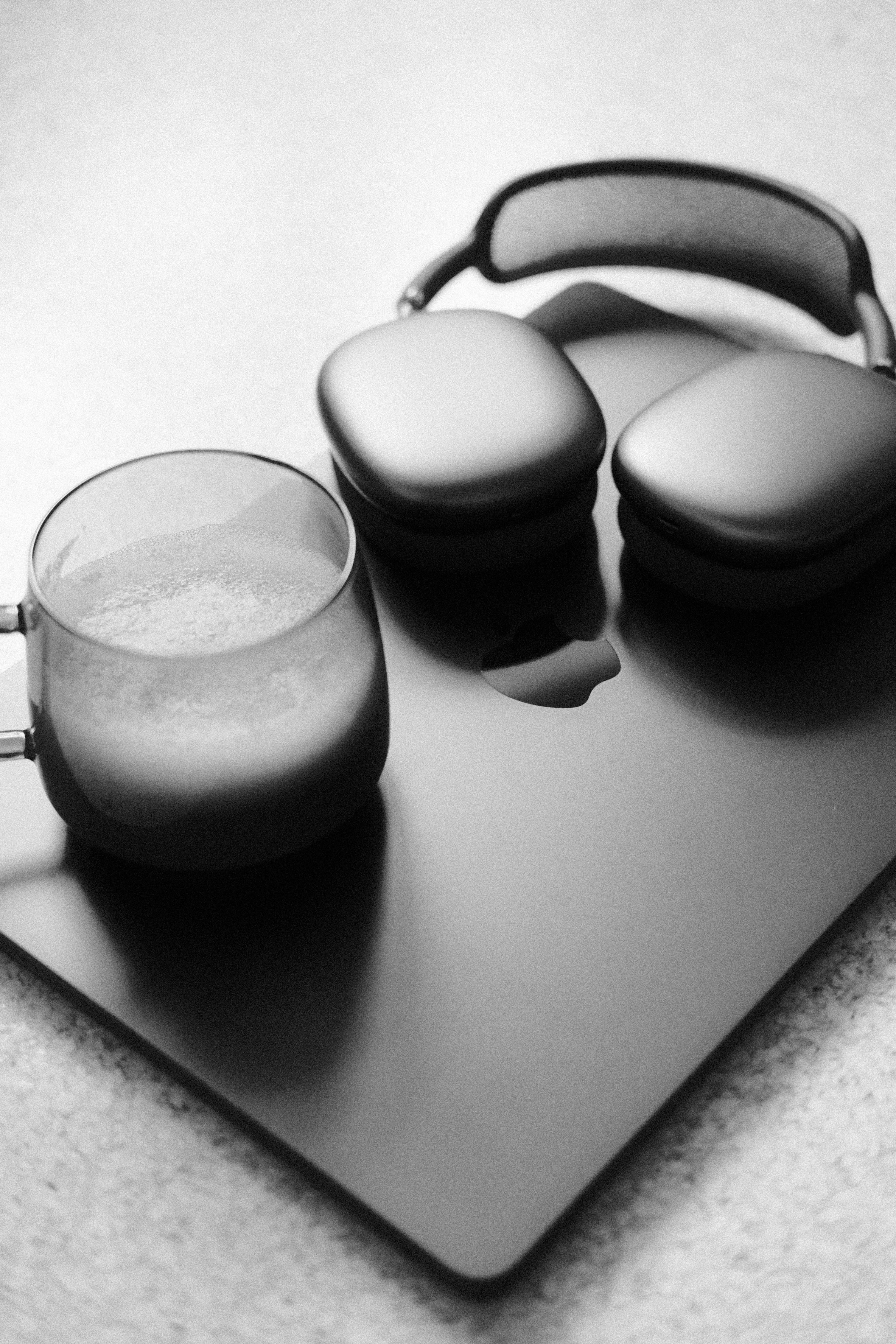 Monochrome Confluence: Cup, Headphones, and the Laptop’s Quiet Apple Emblem