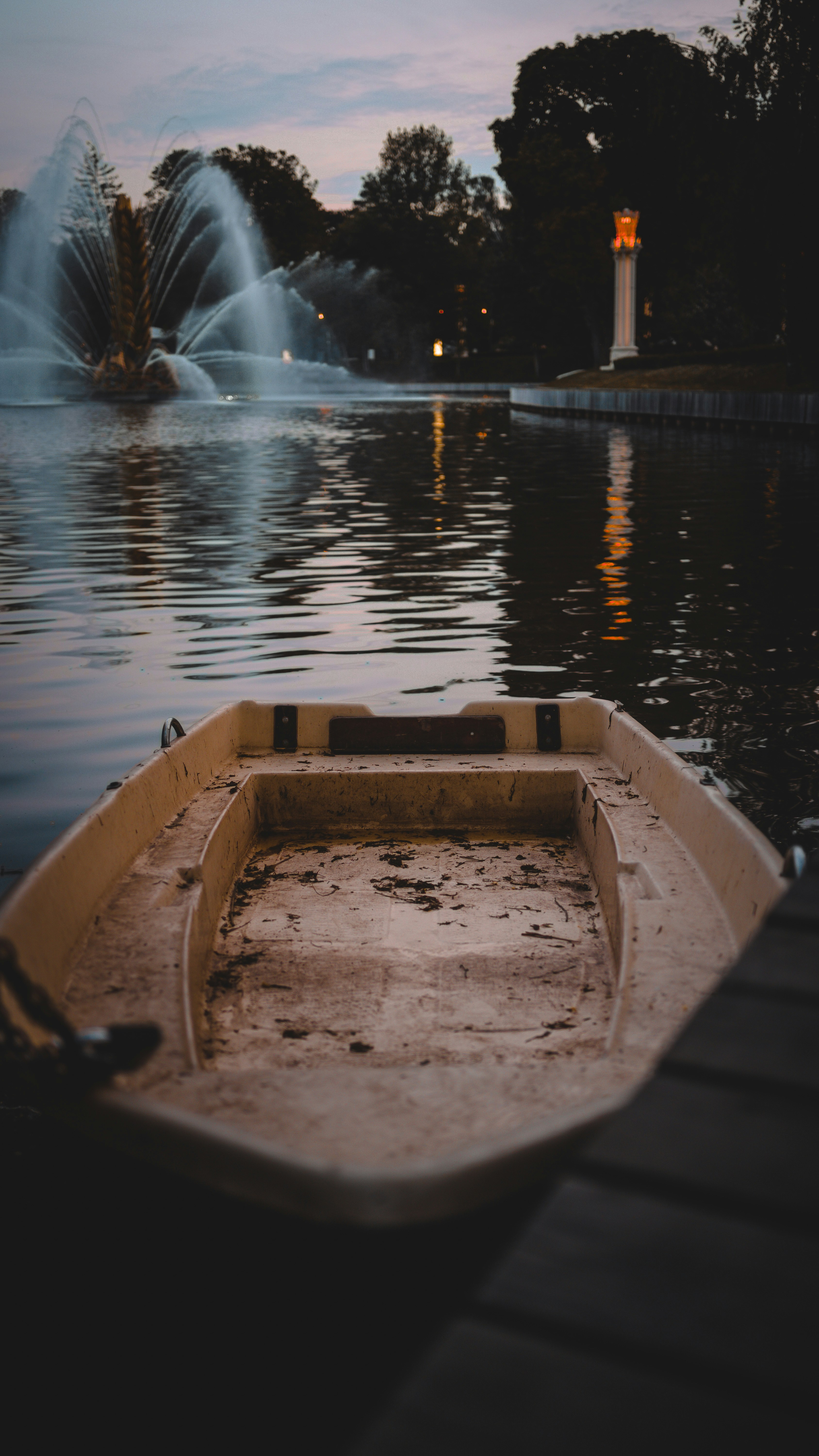 Edge-lit Dusk: A Weathered Rowboat Meets a Fountain-Lit Pond
