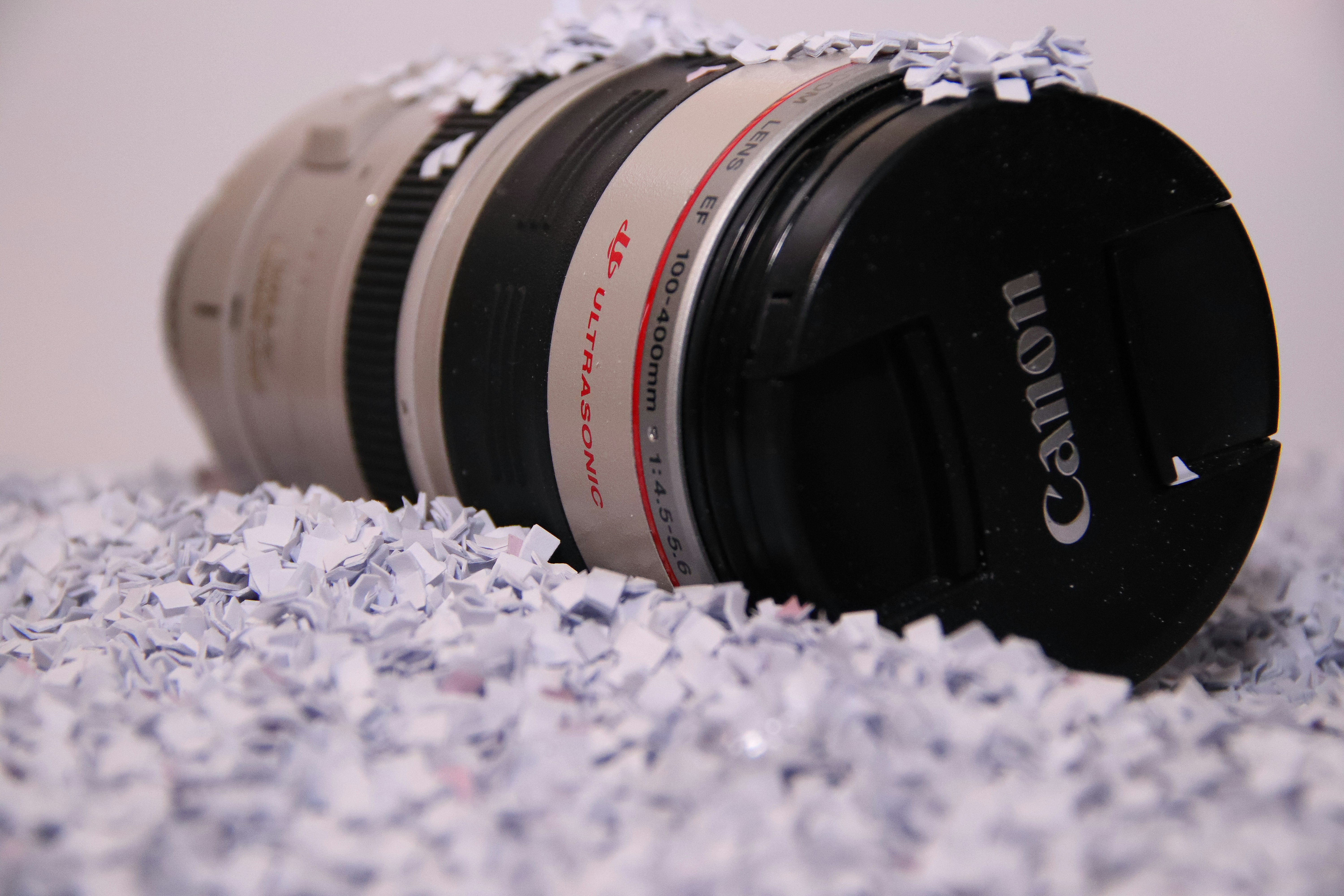 A camera lens laying on top of a pile of shredded paper photo – Free ...