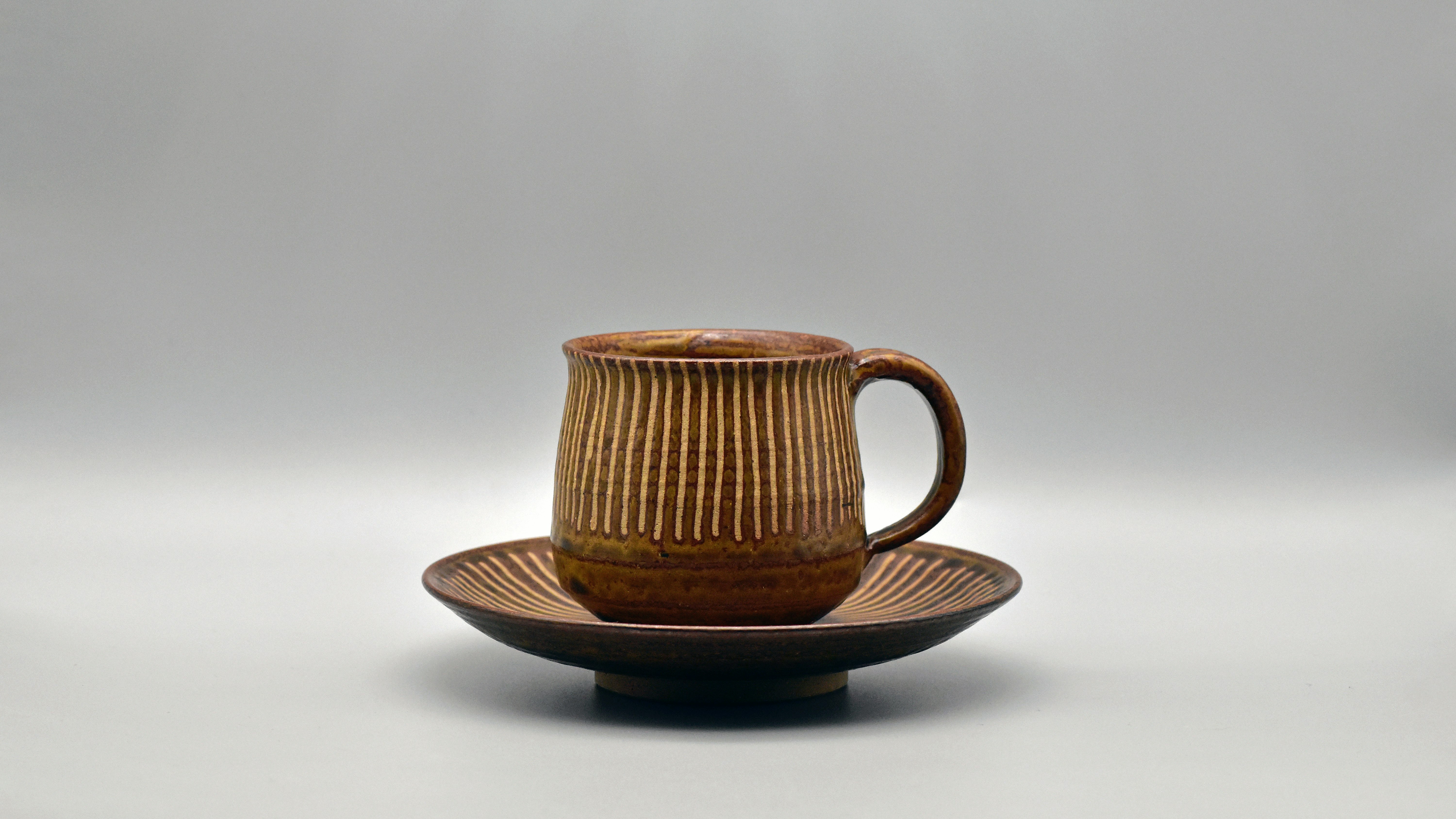 Handcrafted ceramic mug with textured stripes resting on a matching plate, showcasing warm earthy colors.