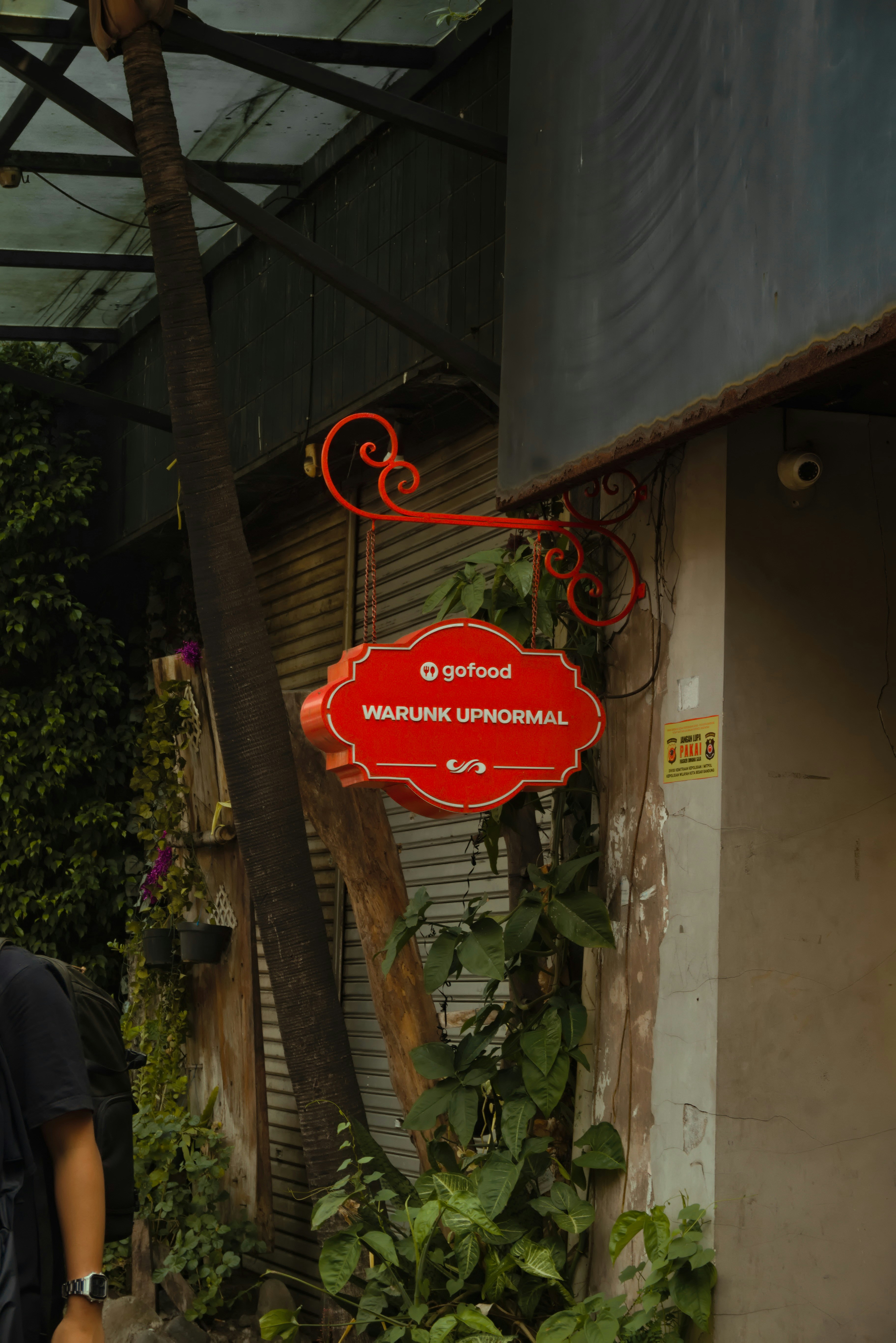 Ornate Red GoFood Sign Framing a Green-Vined Warung Entrance