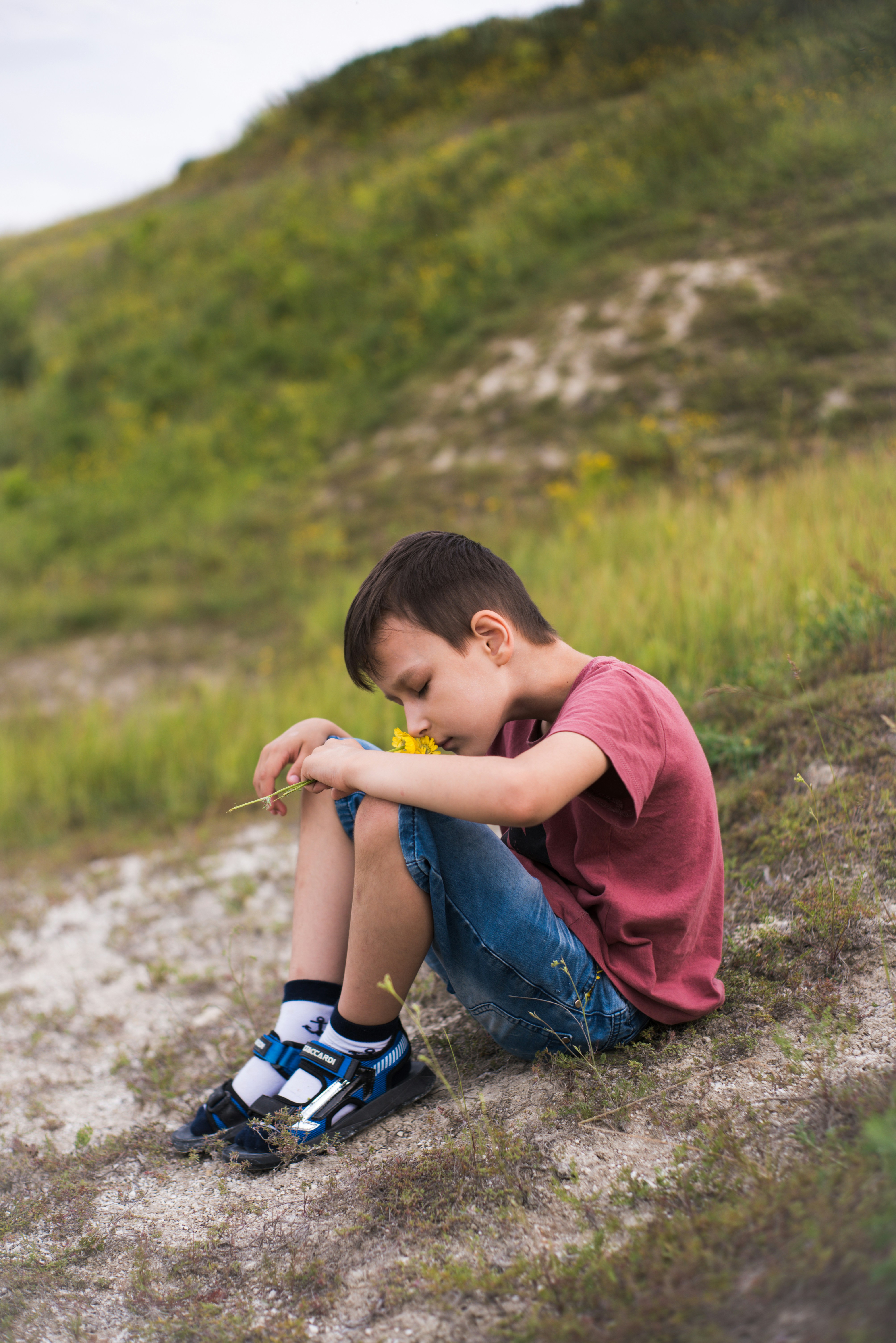 Solitary Moment: A Boy in a Crimson Shirt amidst a Quiet Hill