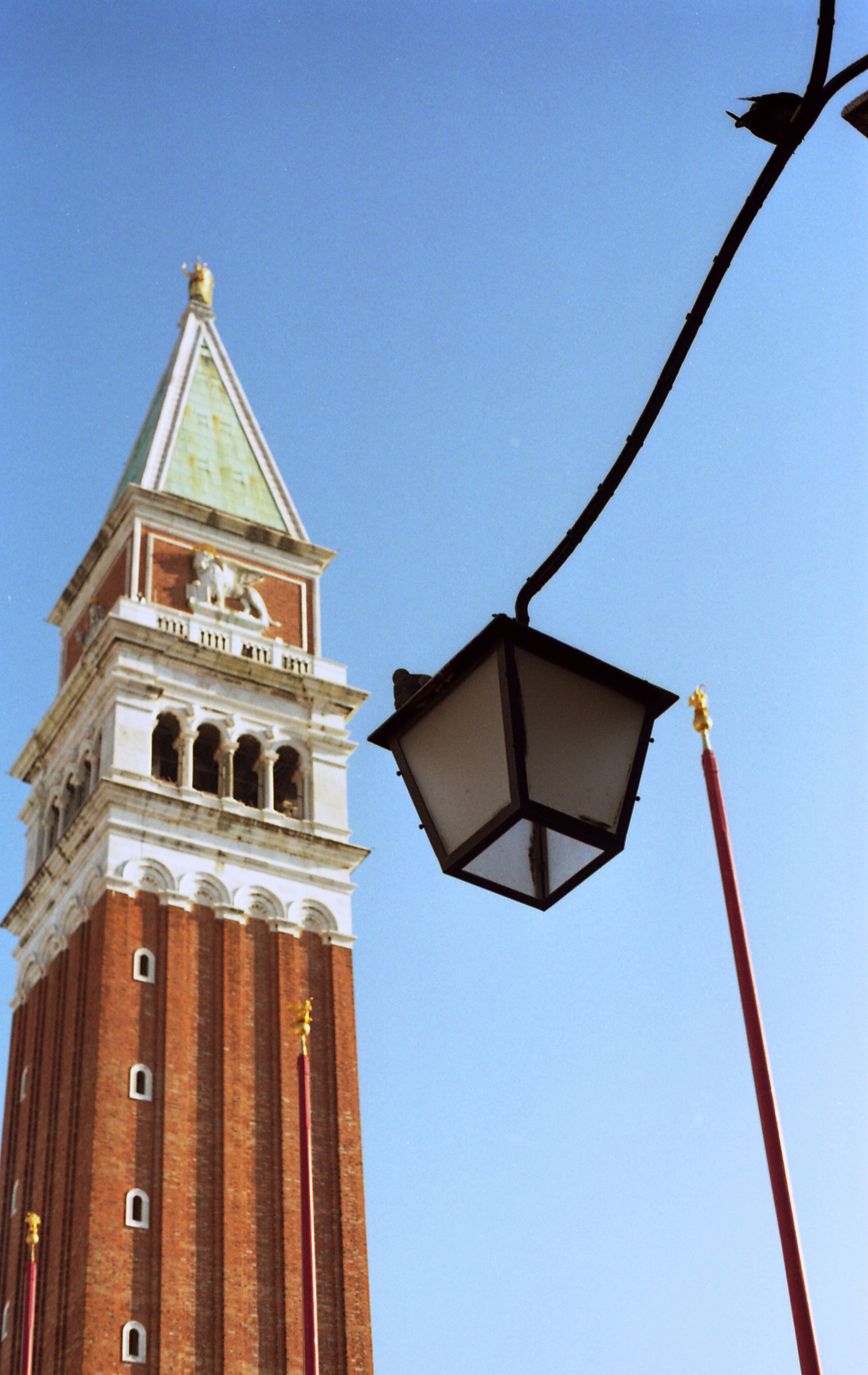 Photograph of St. Mark's Campanile in Venice with a hanging lantern in the foreground against a vivid blue sky.