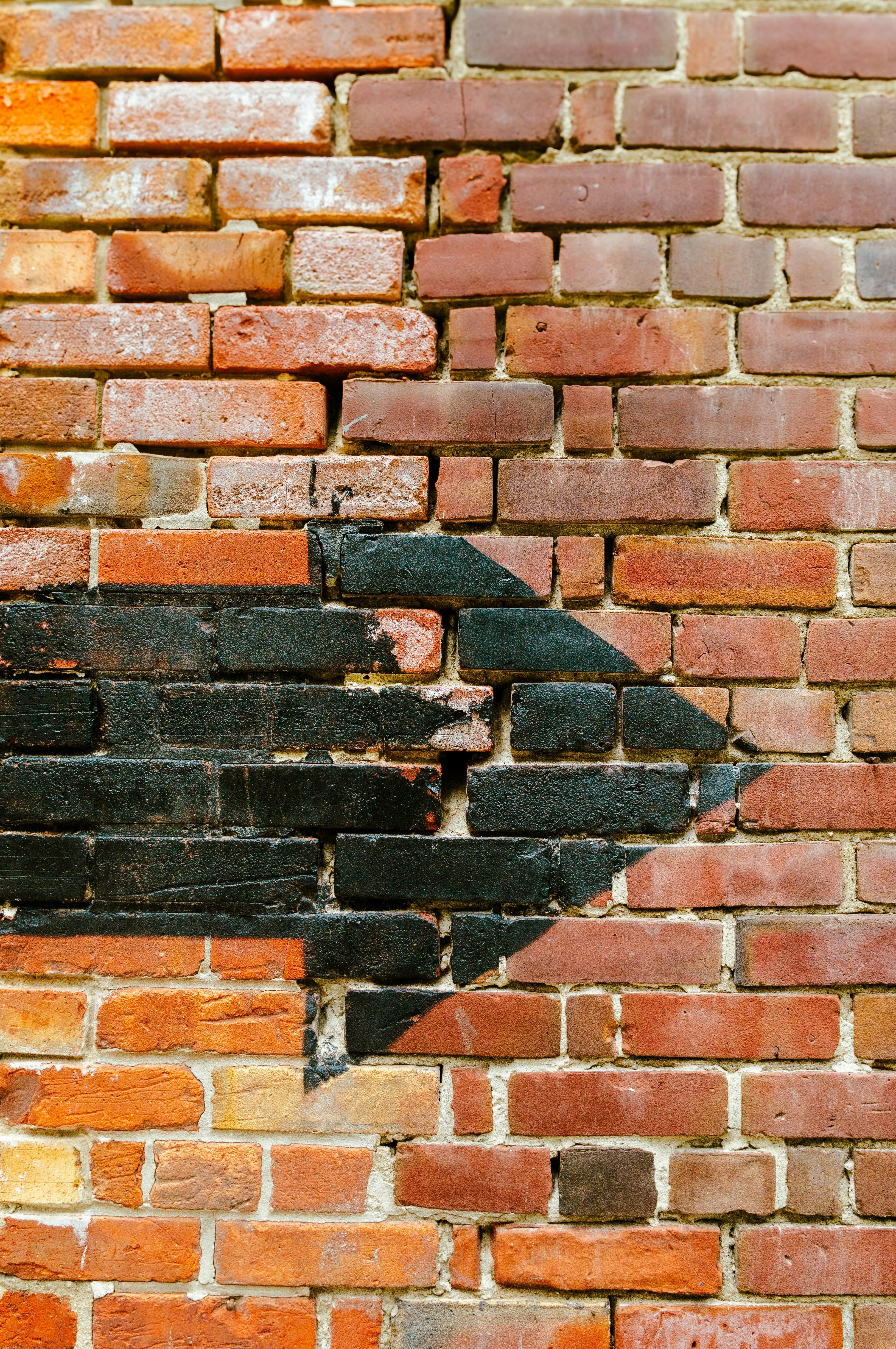 A weathered brick wall features a bold, heart-shaped pattern formed by darker bricks. The composition contrasts warm red hues with a stark black silhouette.