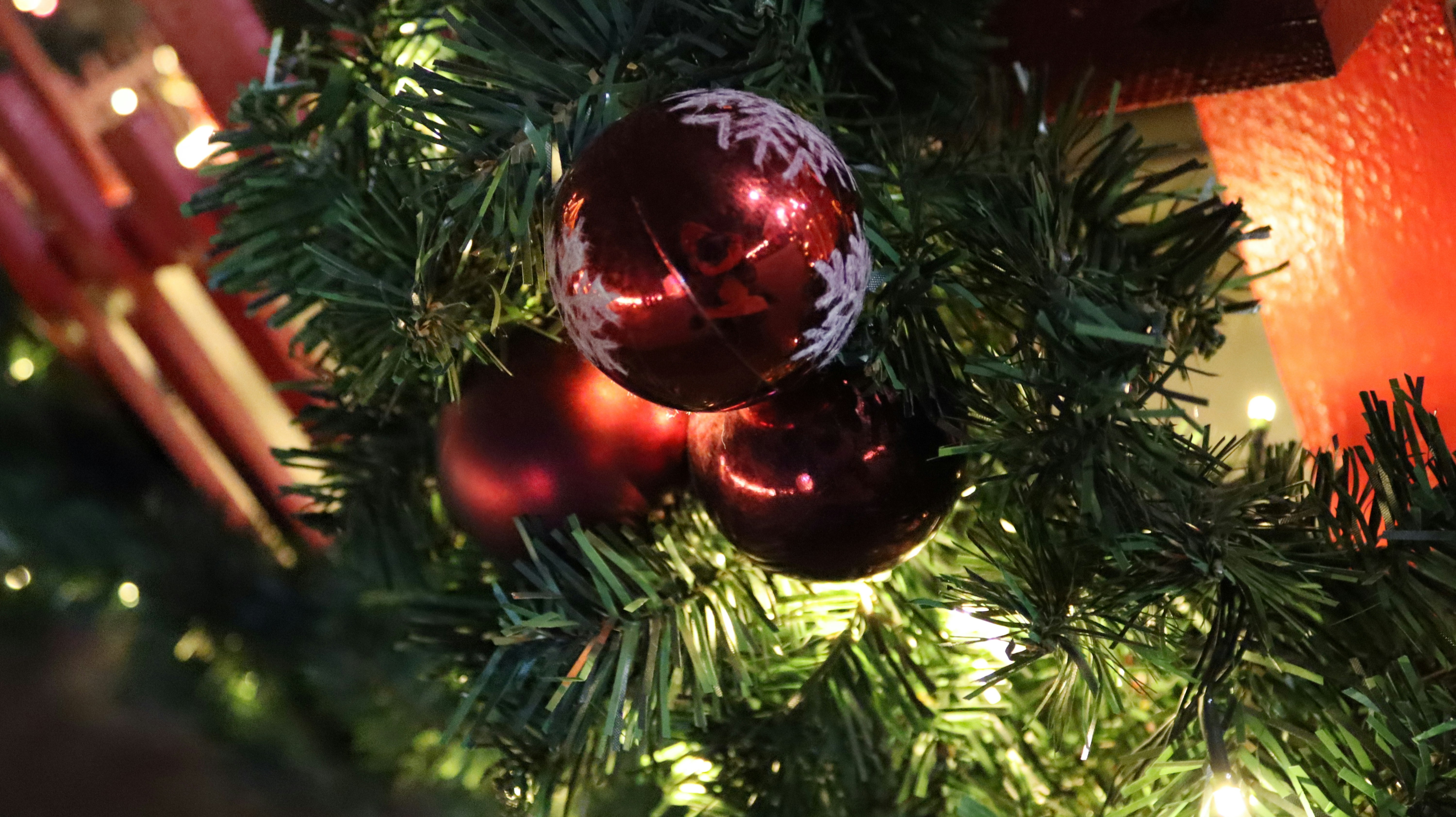 Close-up of a glossy red Christmas bauble with white snowflake pattern nestled among pine needles and warm string lights.
