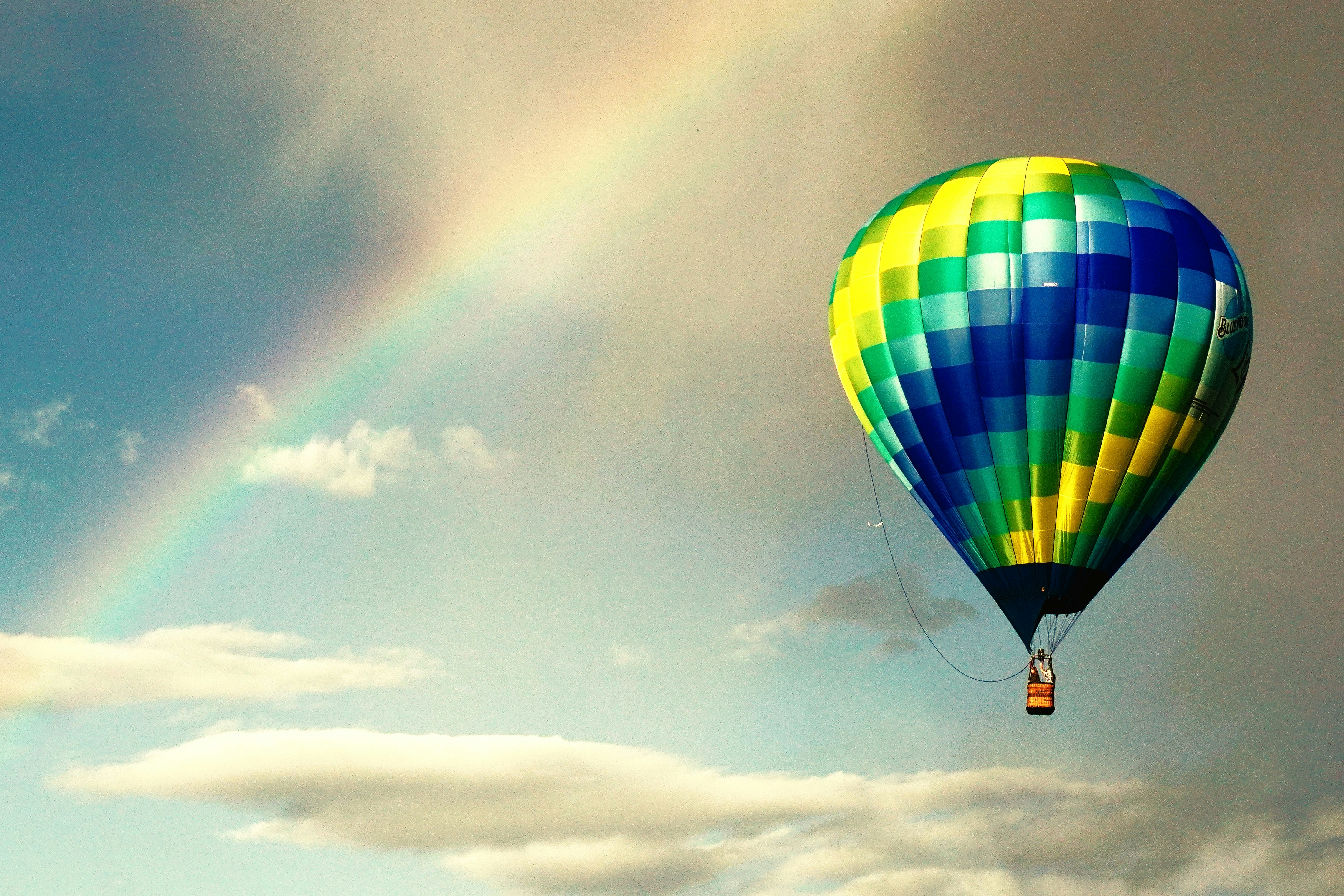 Prismatic Balloon Drifts Across a Sky Framed by a Faint Rainbow