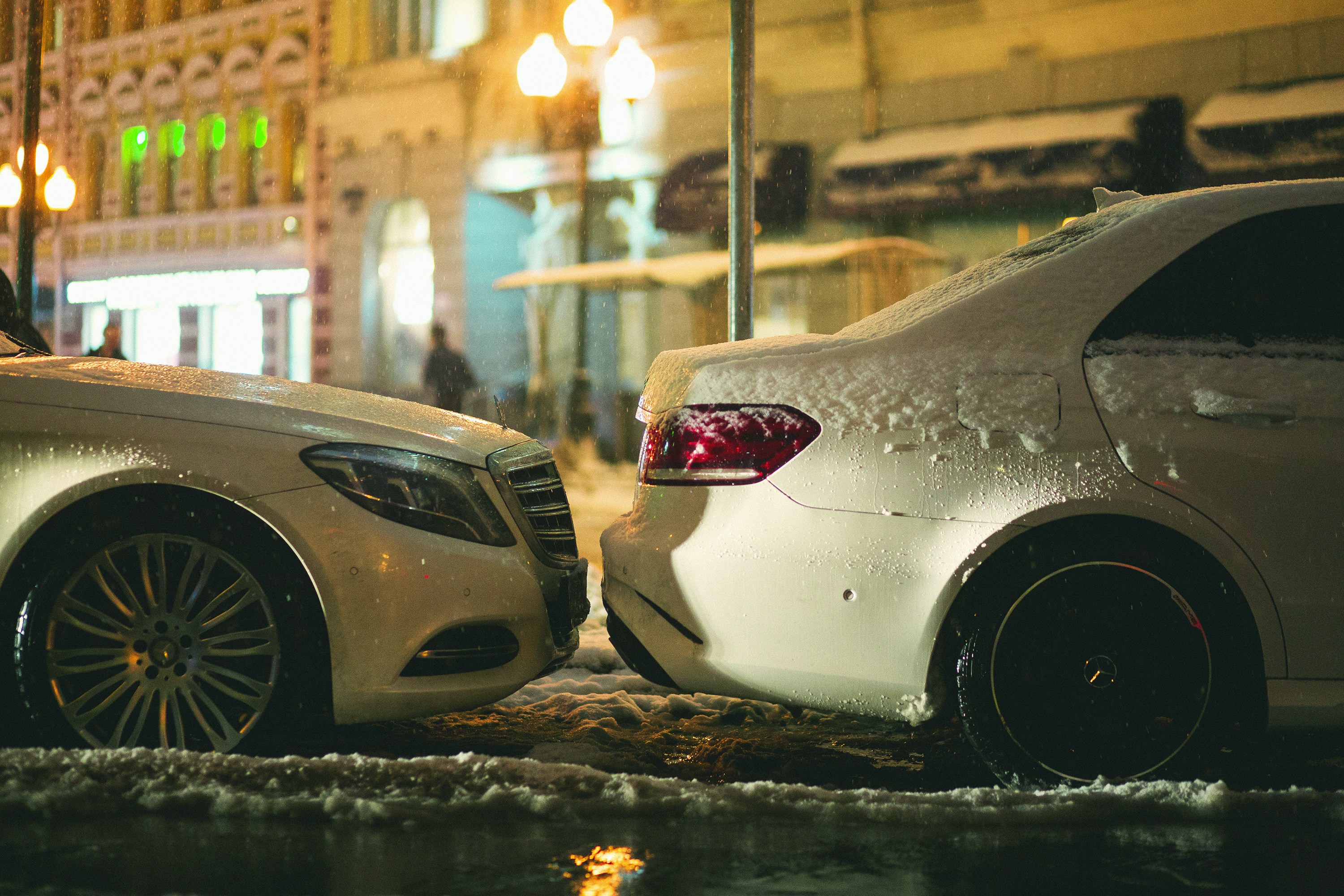 Neon-lit standoff: snow-dusted luxury sedans under urban glow